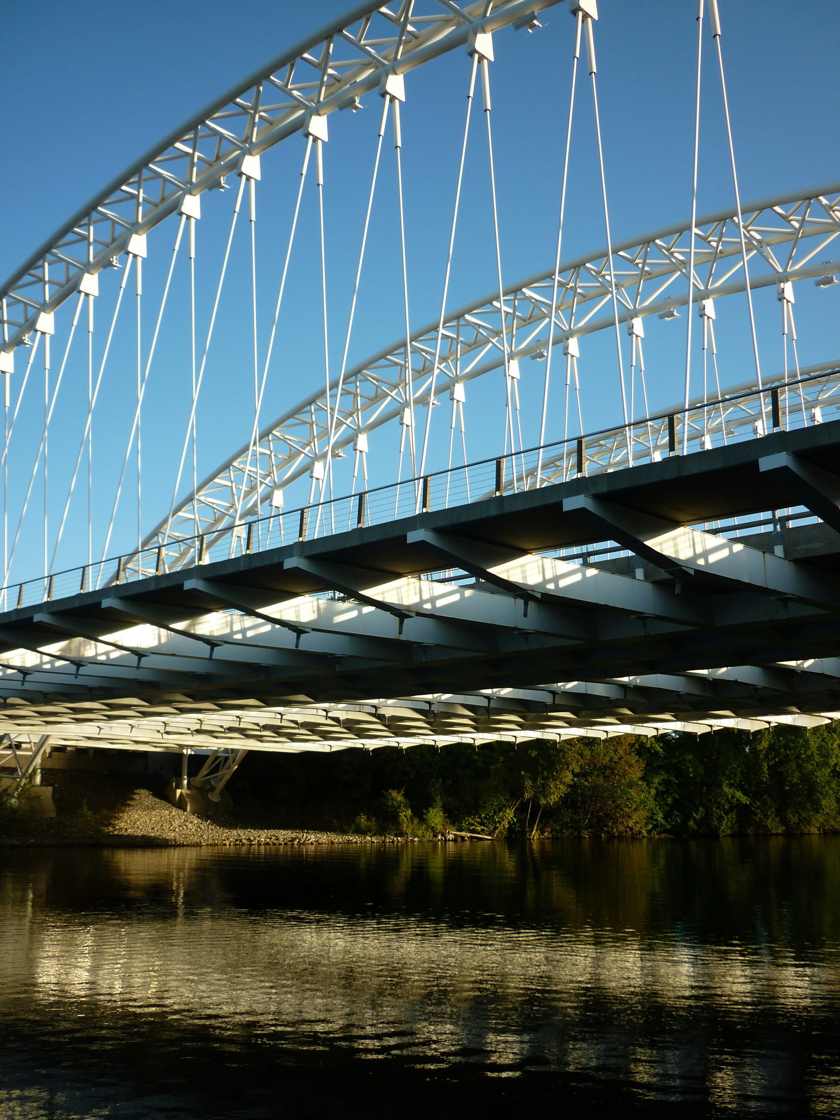 Modern bridge arches over calm water at sunset.