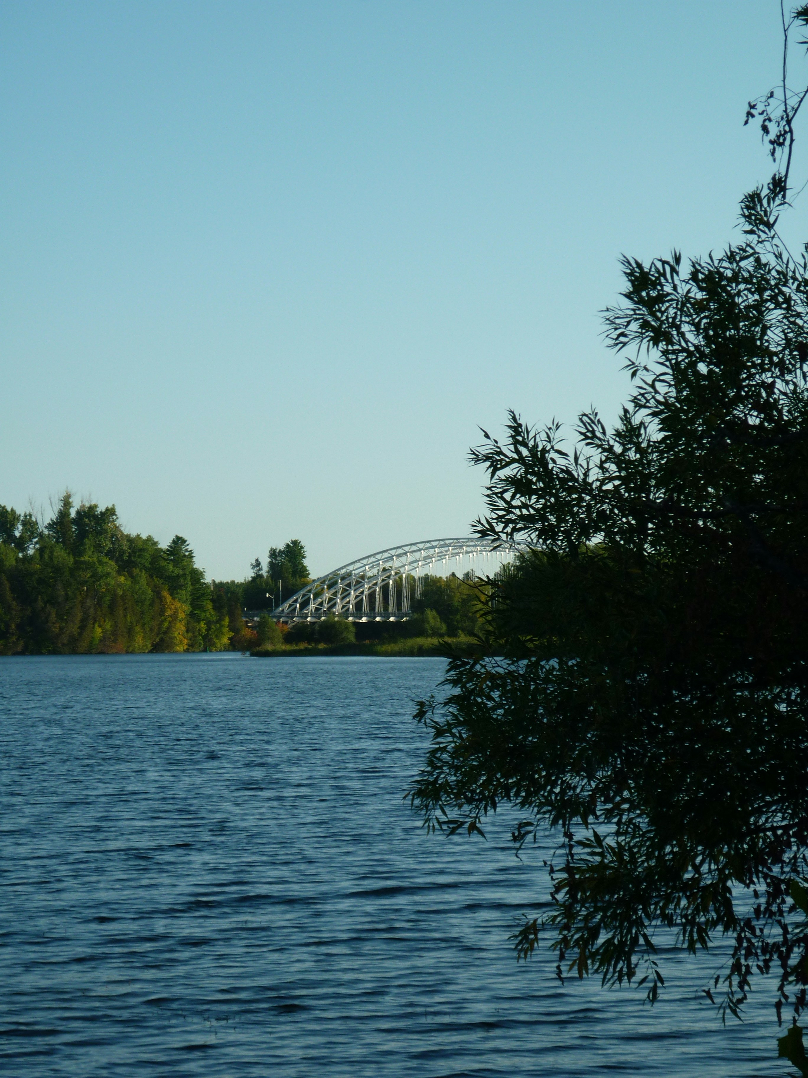White bridge over blue water with trees.