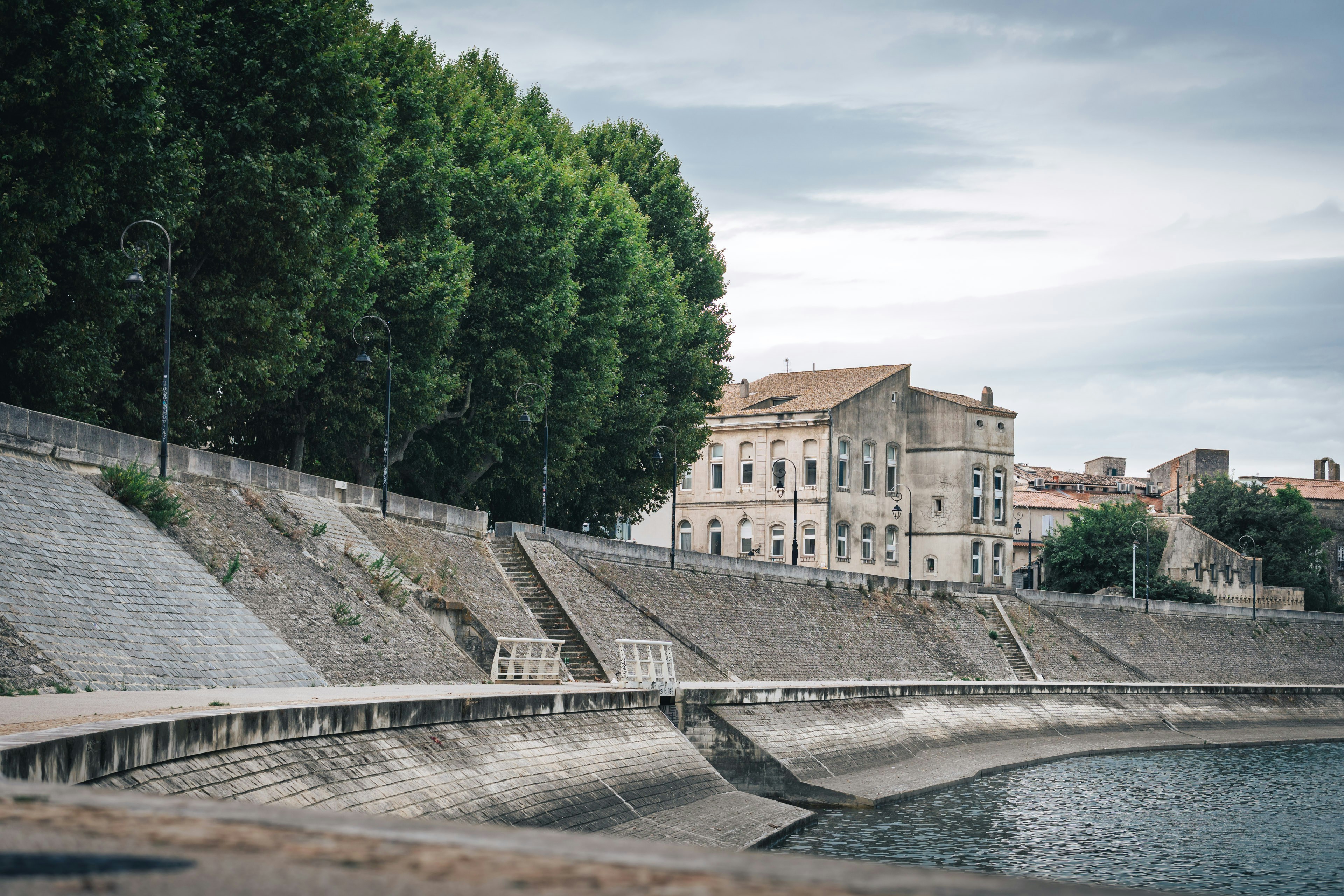 Stone embankment with trees and old building by water. photo – Free ...