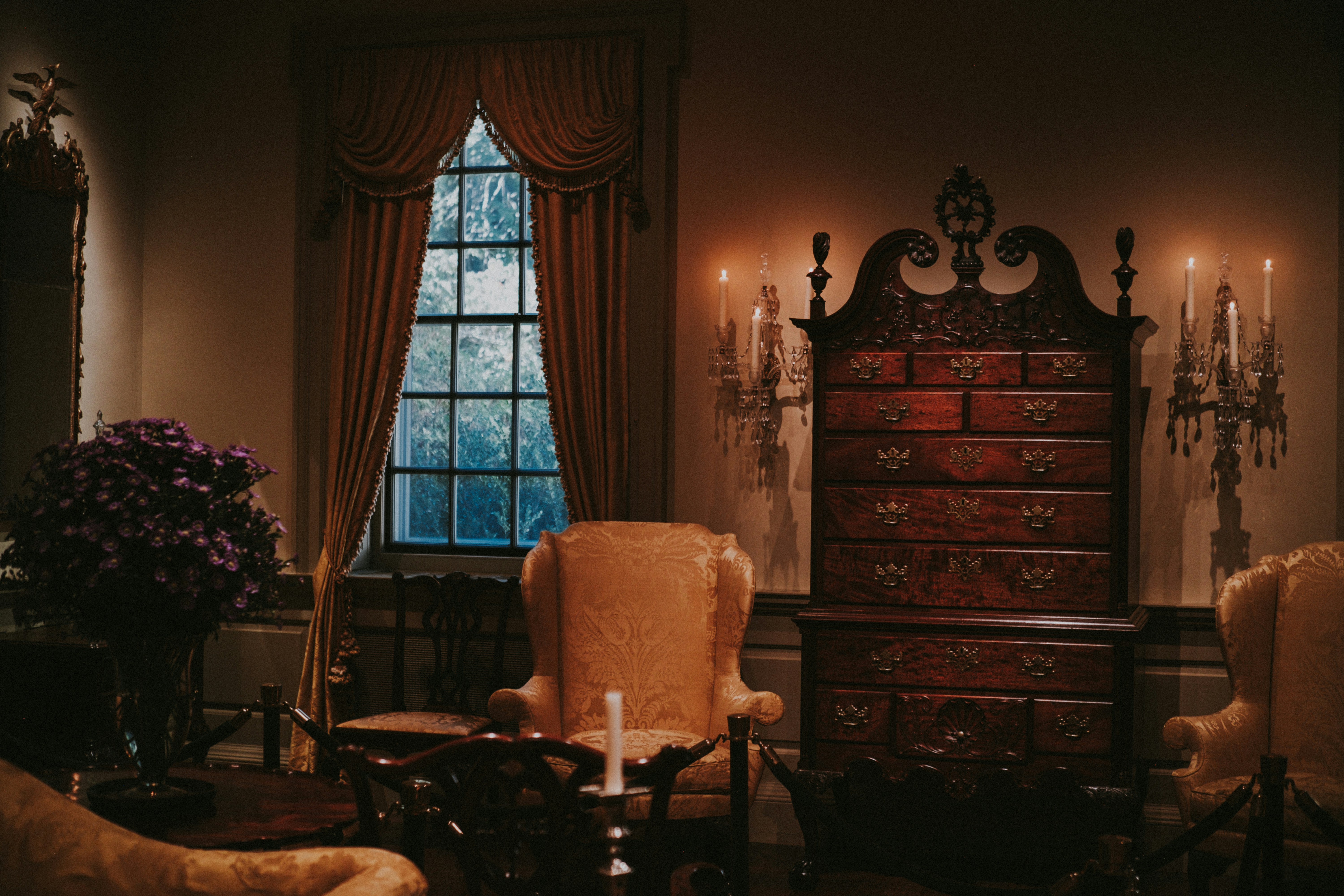 Richly decorated room featuring ornate furniture, a vintage chest of drawers, and elegant drapery, illuminated by soft candlelight.