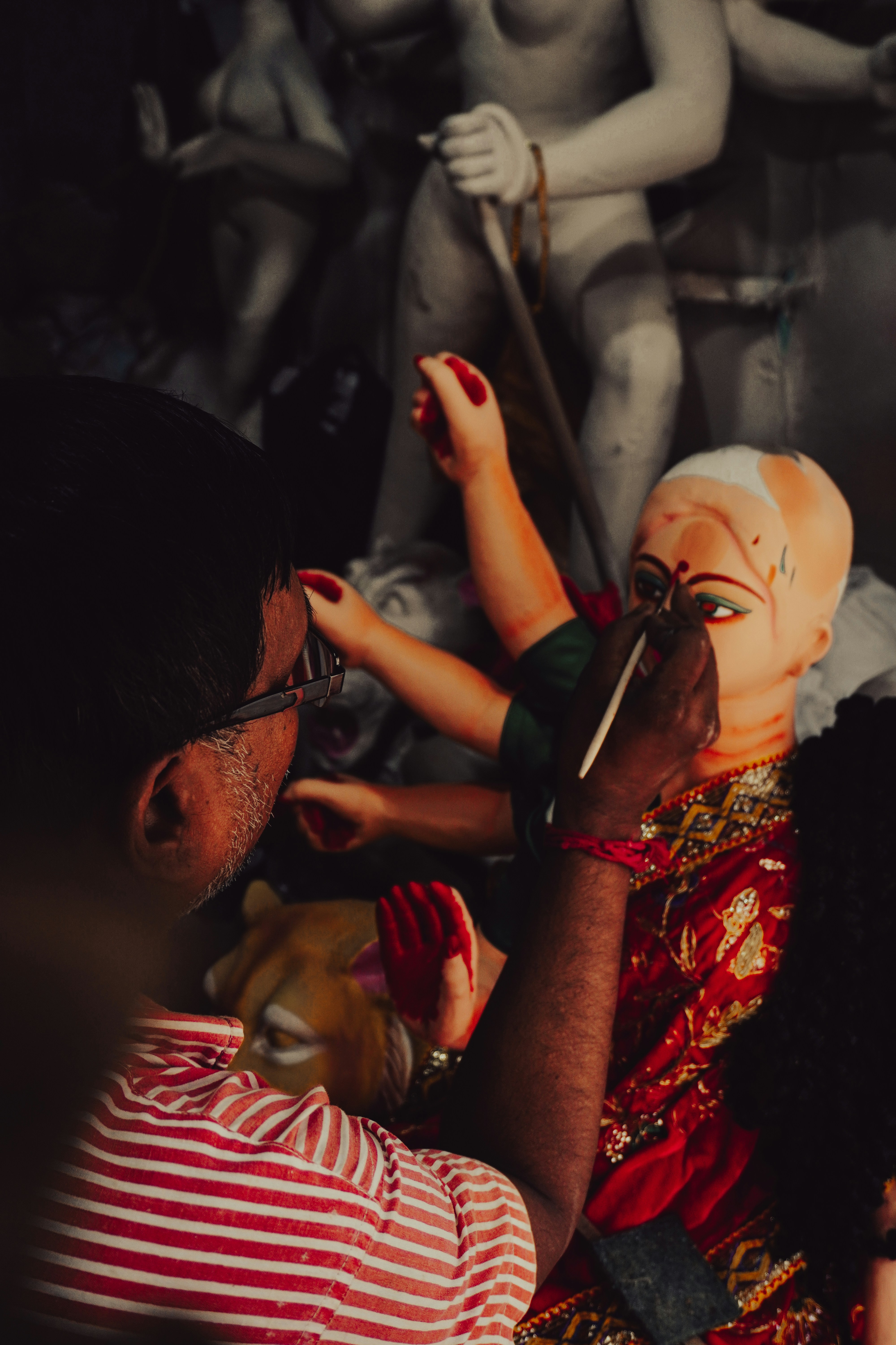 Artisan meticulously painting the features of a deity idol, surrounded by partially finished sculptures in a workshop.