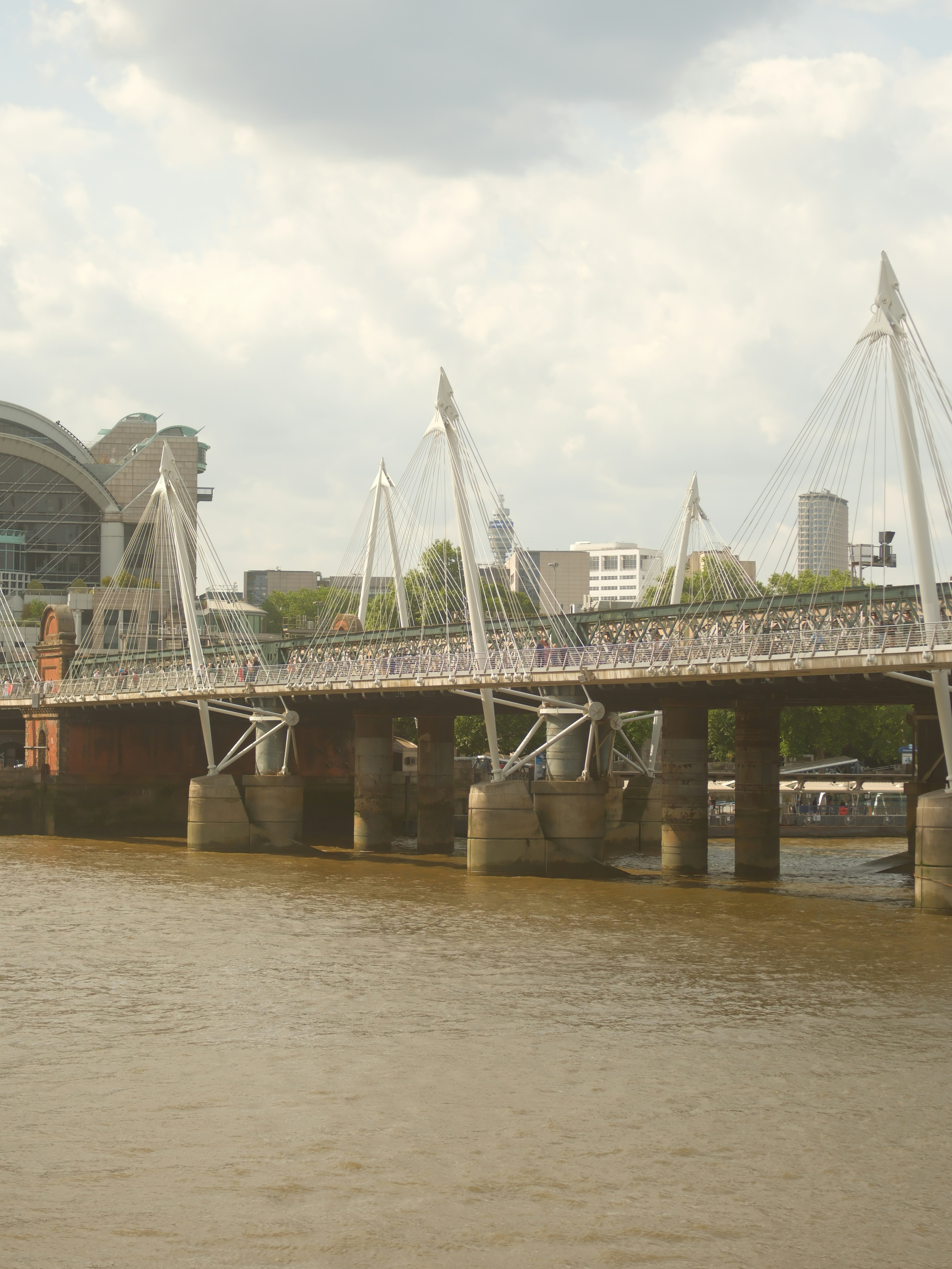 A cable-stayed bridge spans the River Thames, showcasing modern architecture against an urban backdrop. The scene captures the dynamic interaction between nature and city life.