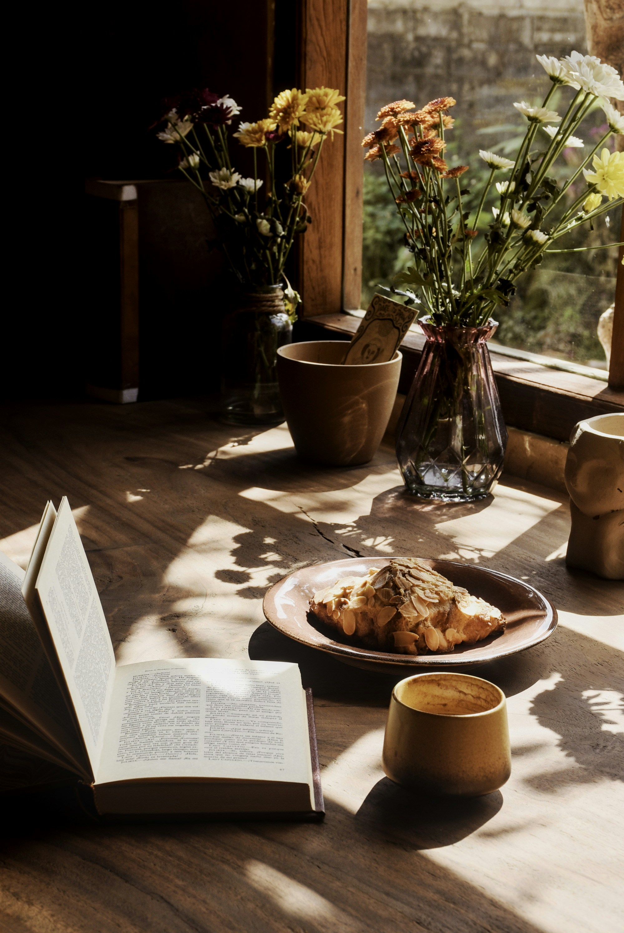 Open book, croissant, and coffee by window.