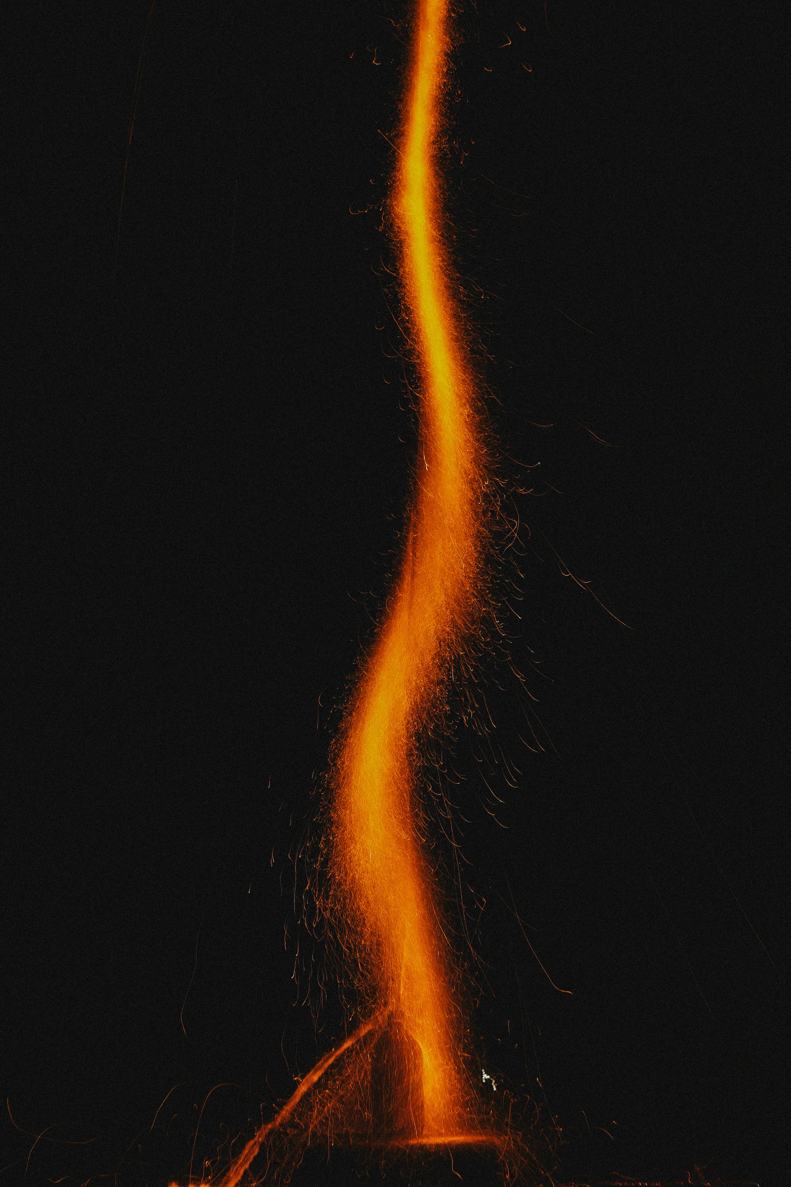 A bright orange flame erupts upwards against a dark background.