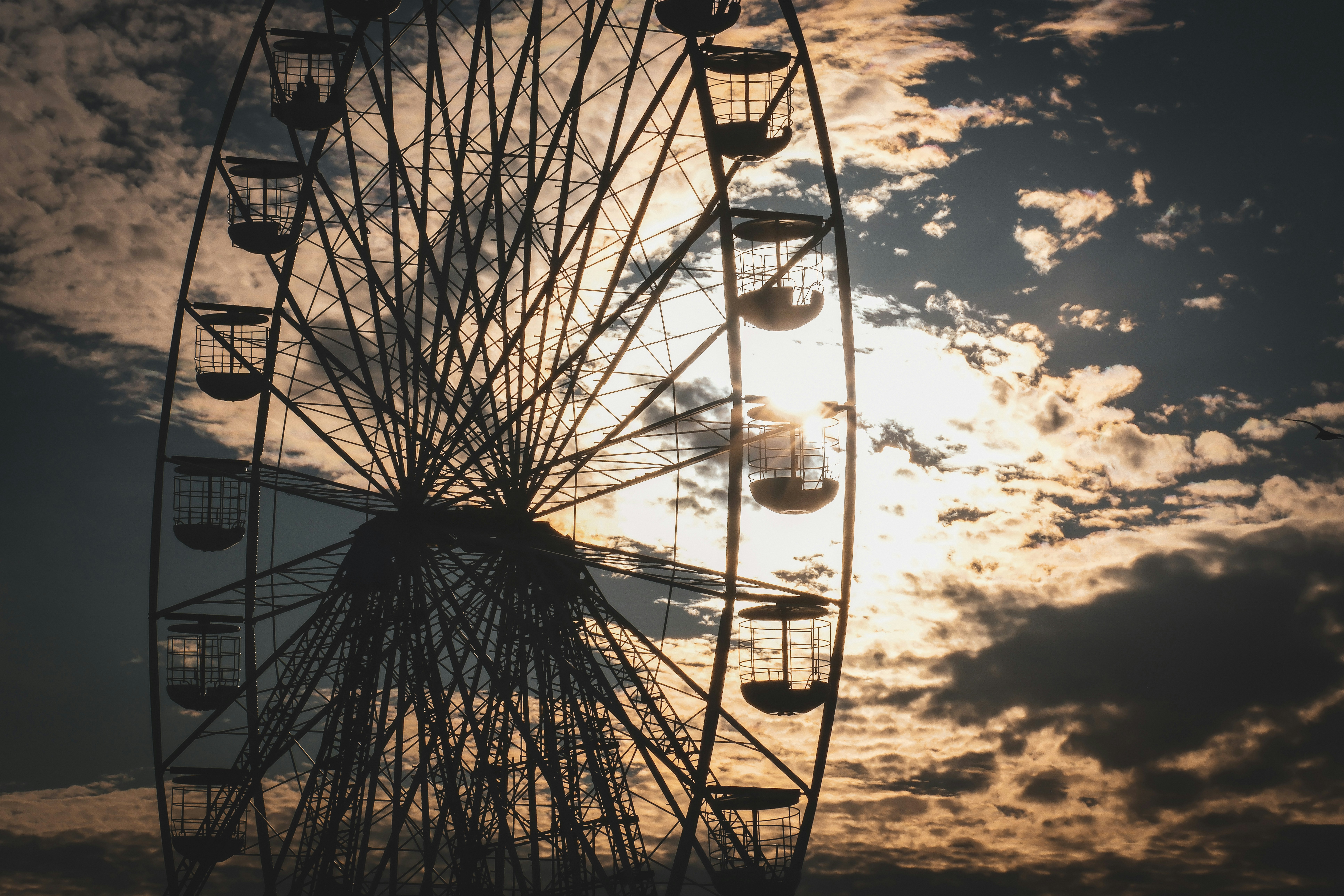 A dramatic Ferris wheel silhouette against a glowing sunset sky. | Ferris wheel silhouetted against dramatic sunset sky