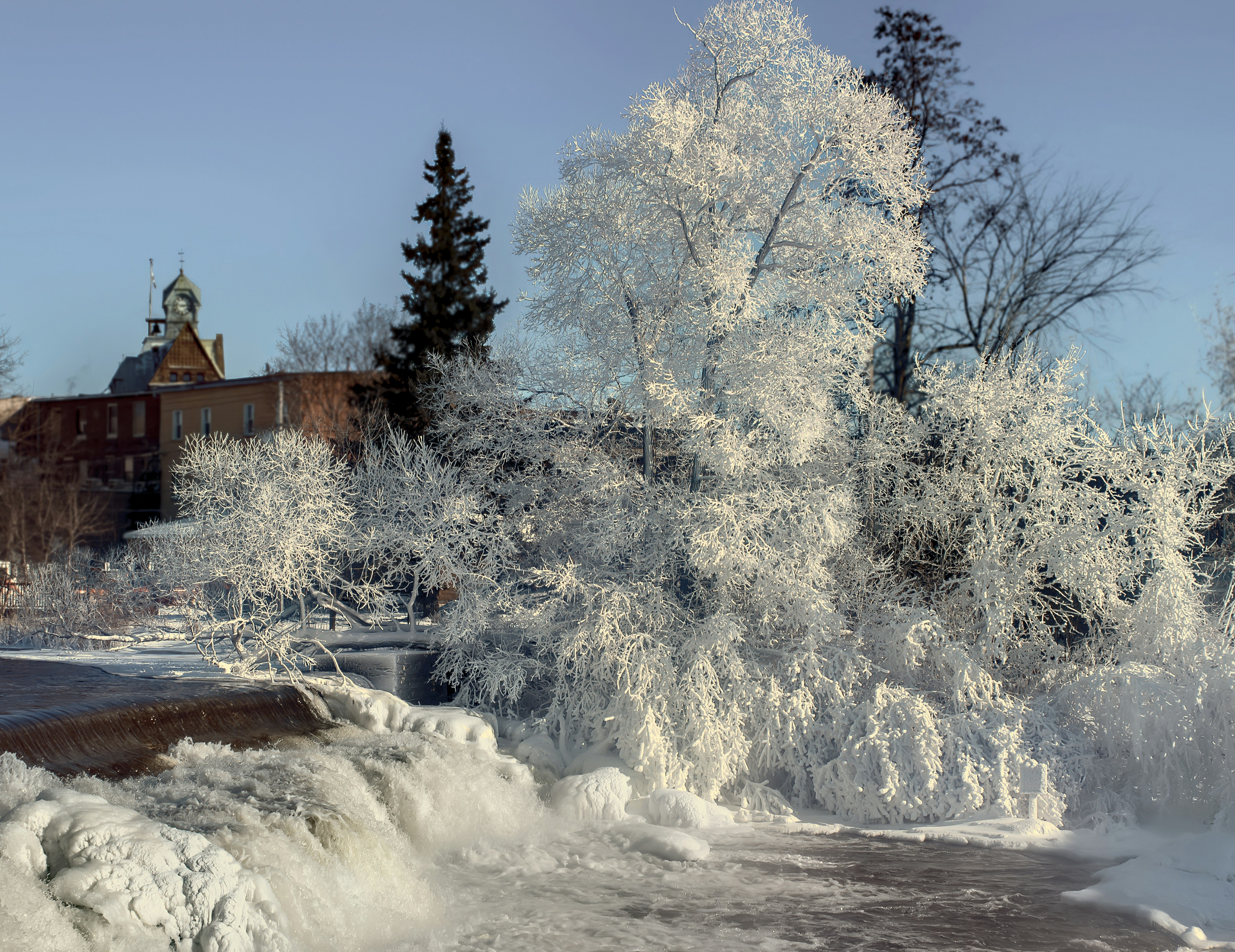 Mother Nature decorates her own Christmas Tree from the mist of the waterfalls. | Frozen trees and building by a flowing river