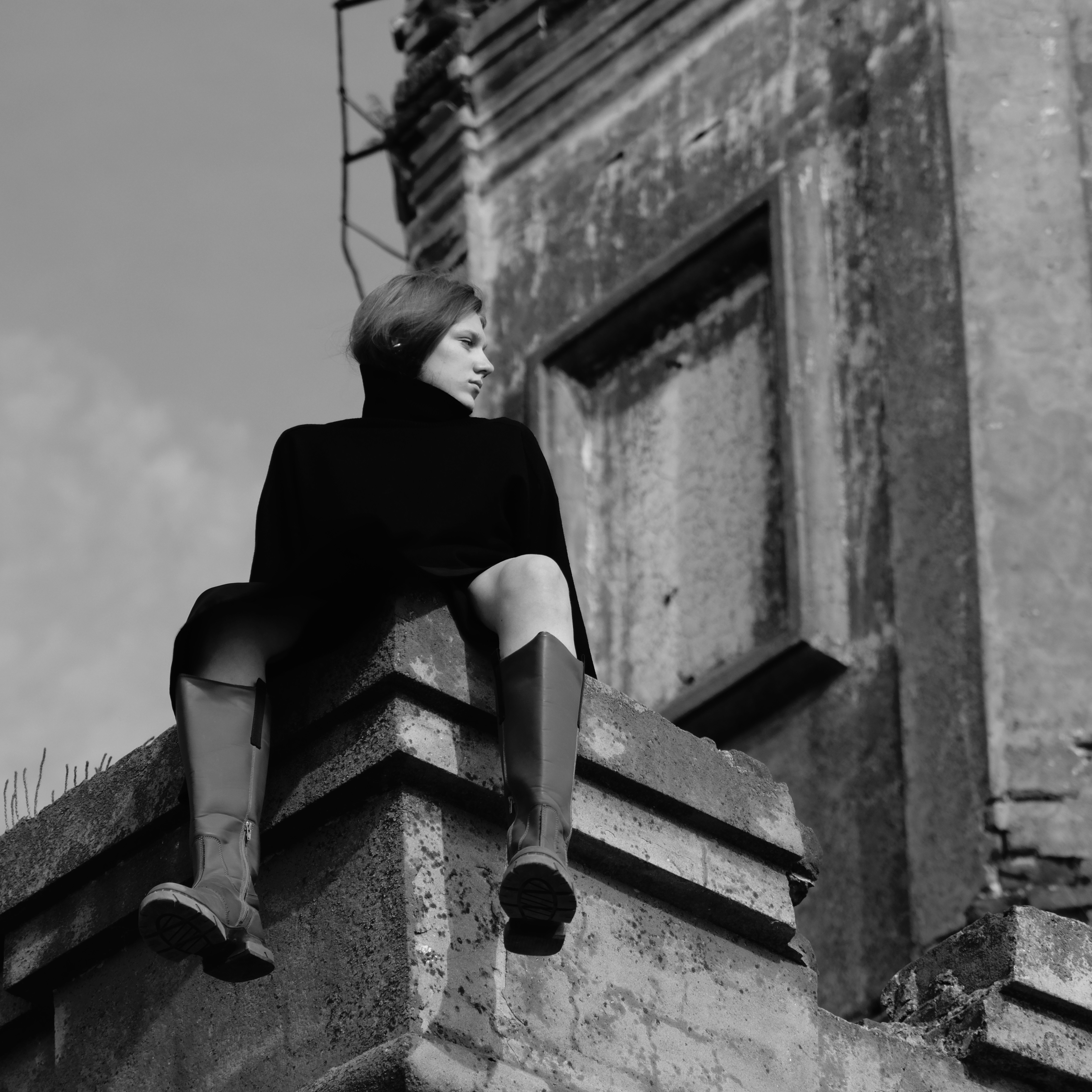 Woman in coat and boots sits on crumbling ledge