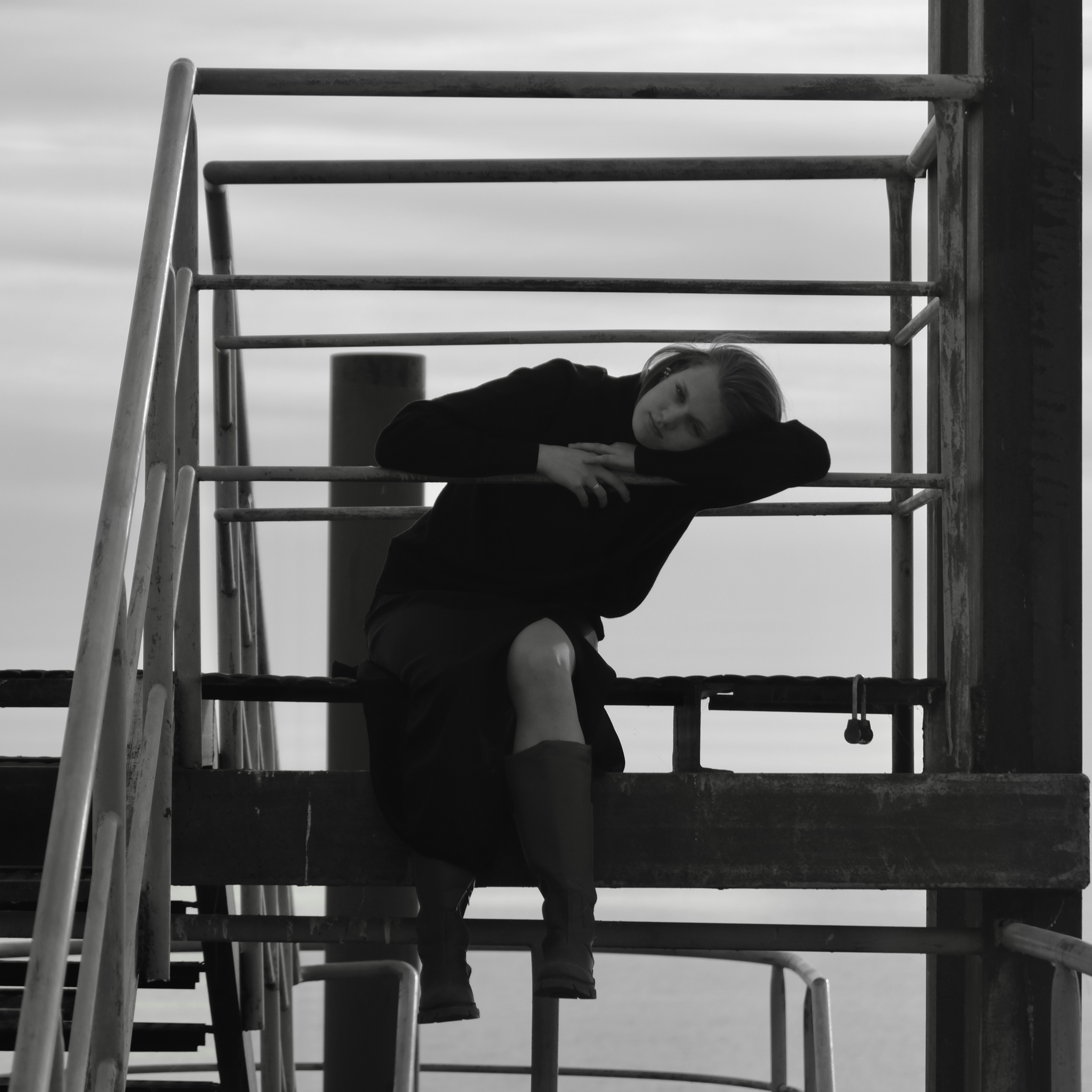 A figure in a black coat rests on a metallic structure, surrounded by soft, diffused light. The scene captures a tranquil yet introspective atmosphere.