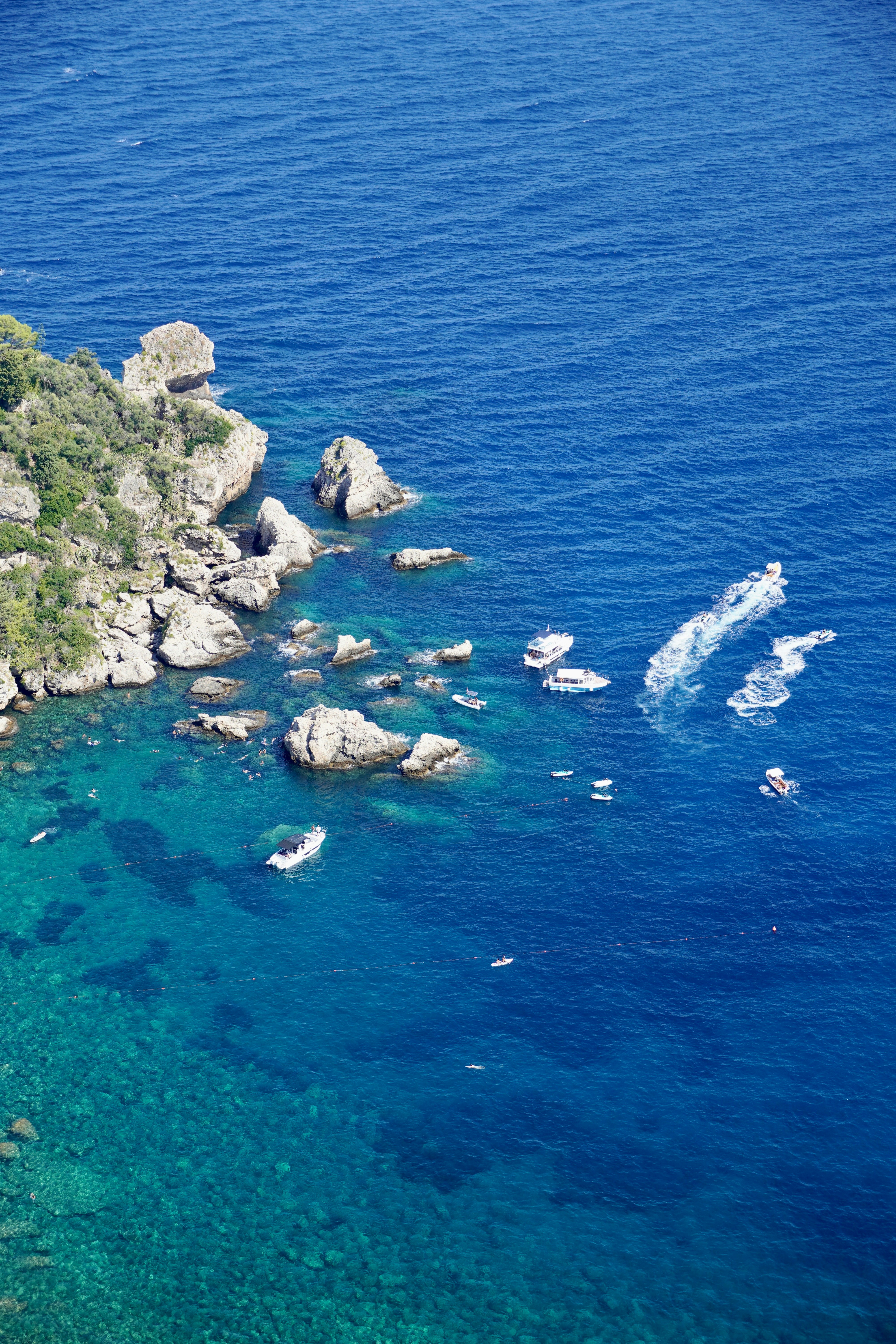 Vibrant turquoise waters meet rocky shores, dotted with boats exploring the coastline. Lush greenery frames the scene, embodying a harmonious blend of nature and leisure.