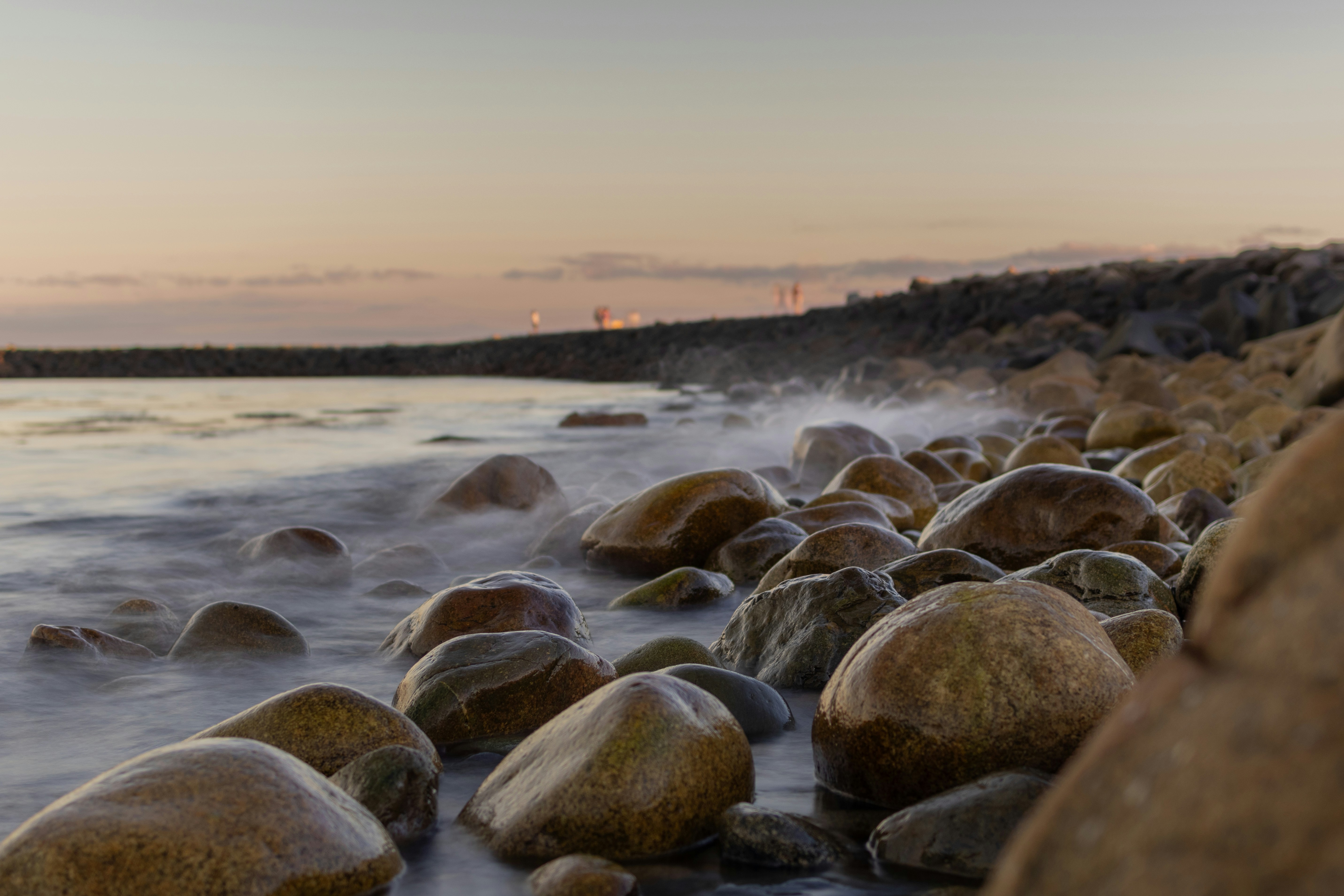 Waves gently lap against wet, smooth stones at sunset.