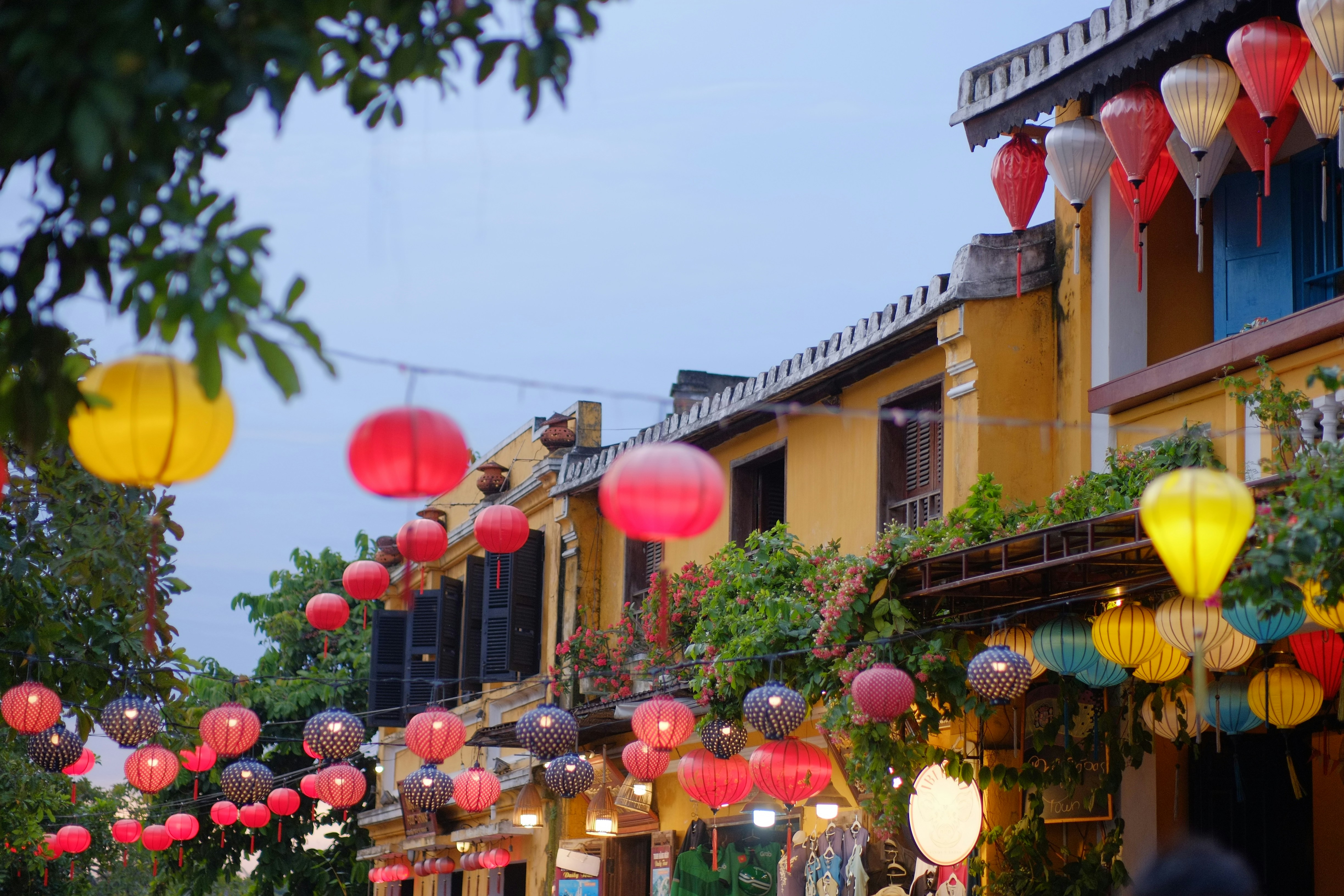 Colorful lanterns hanging above a vibrant street in Hoi An, illuminating the charming architecture as dusk settles.