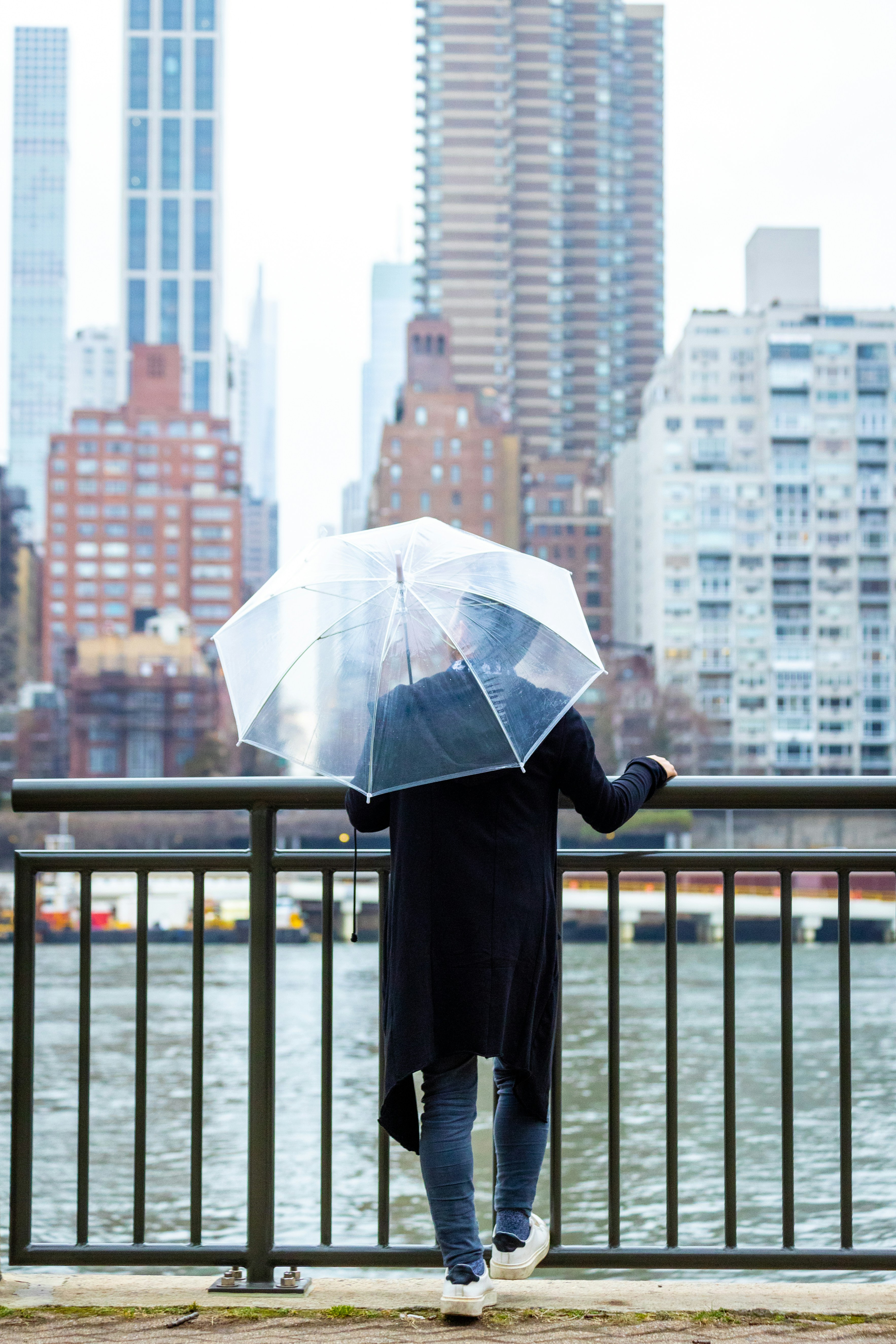 Person with umbrella overlooks city skyline by water