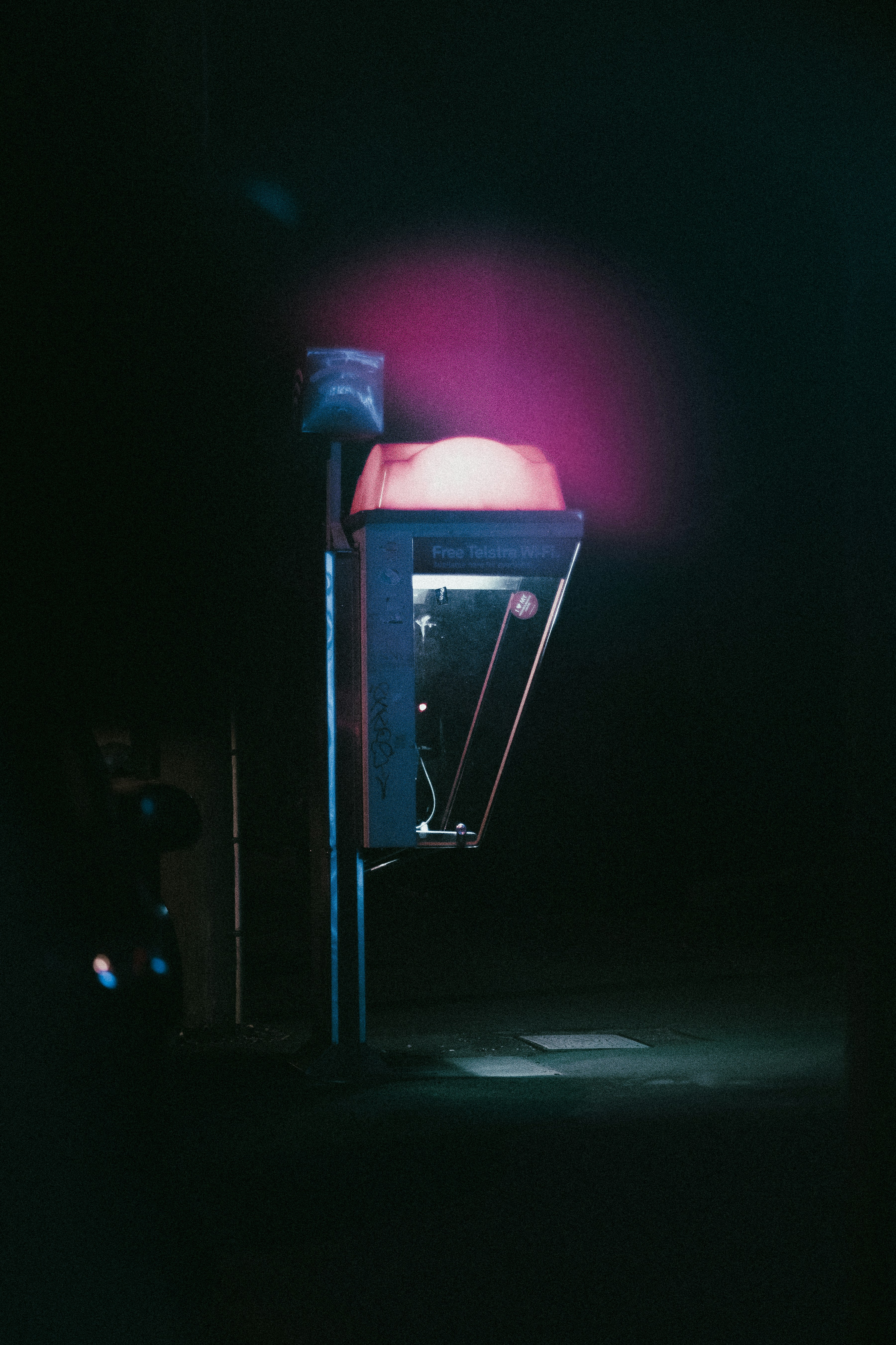 A lonely payphone booth at night with neon lights.
