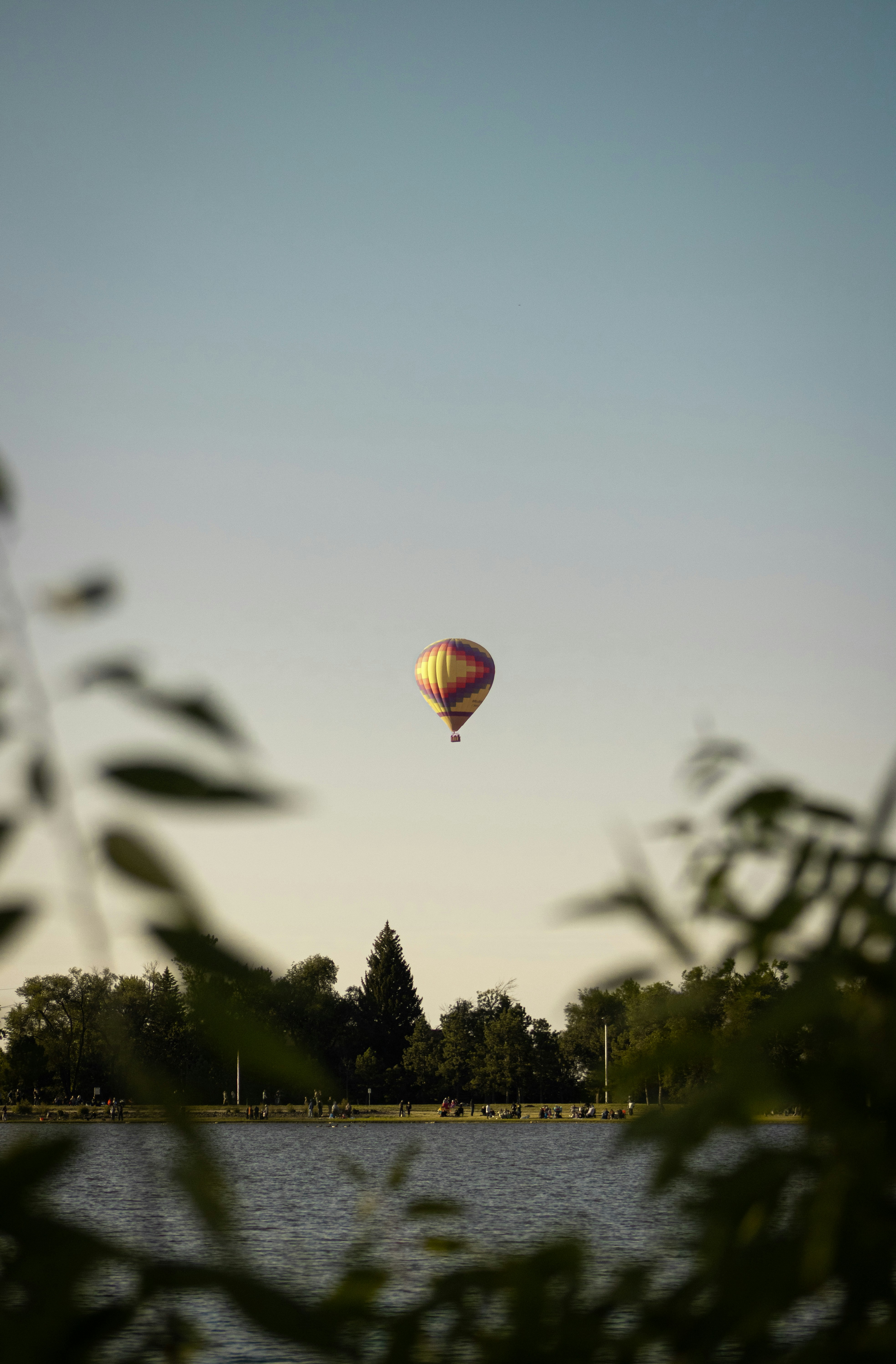 A hot air balloon floats over a lake and trees.