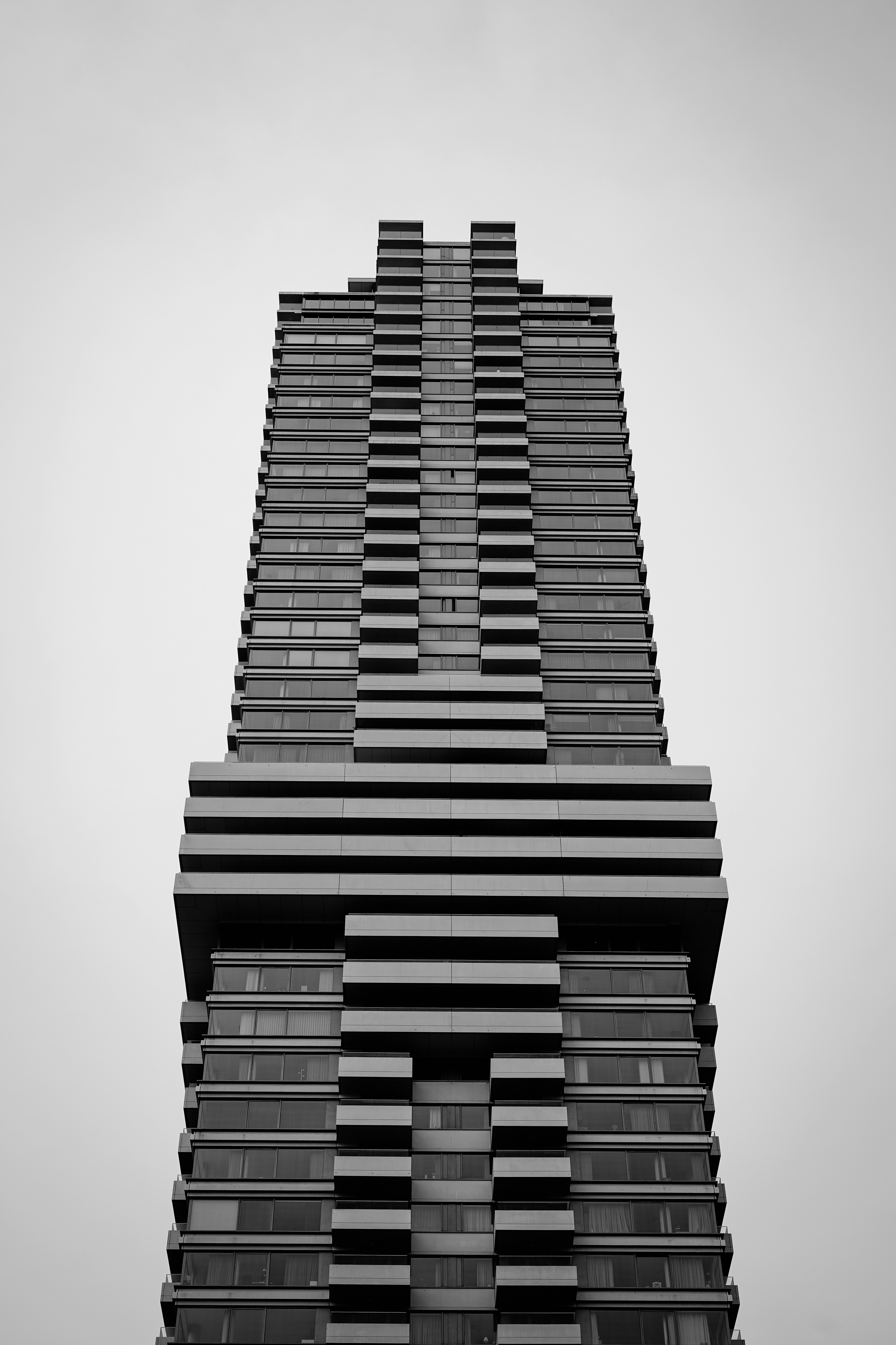 Monochrome photograph of a towering residential building with a striking geometric facade. The design emphasizes clean lines and layered balconies.