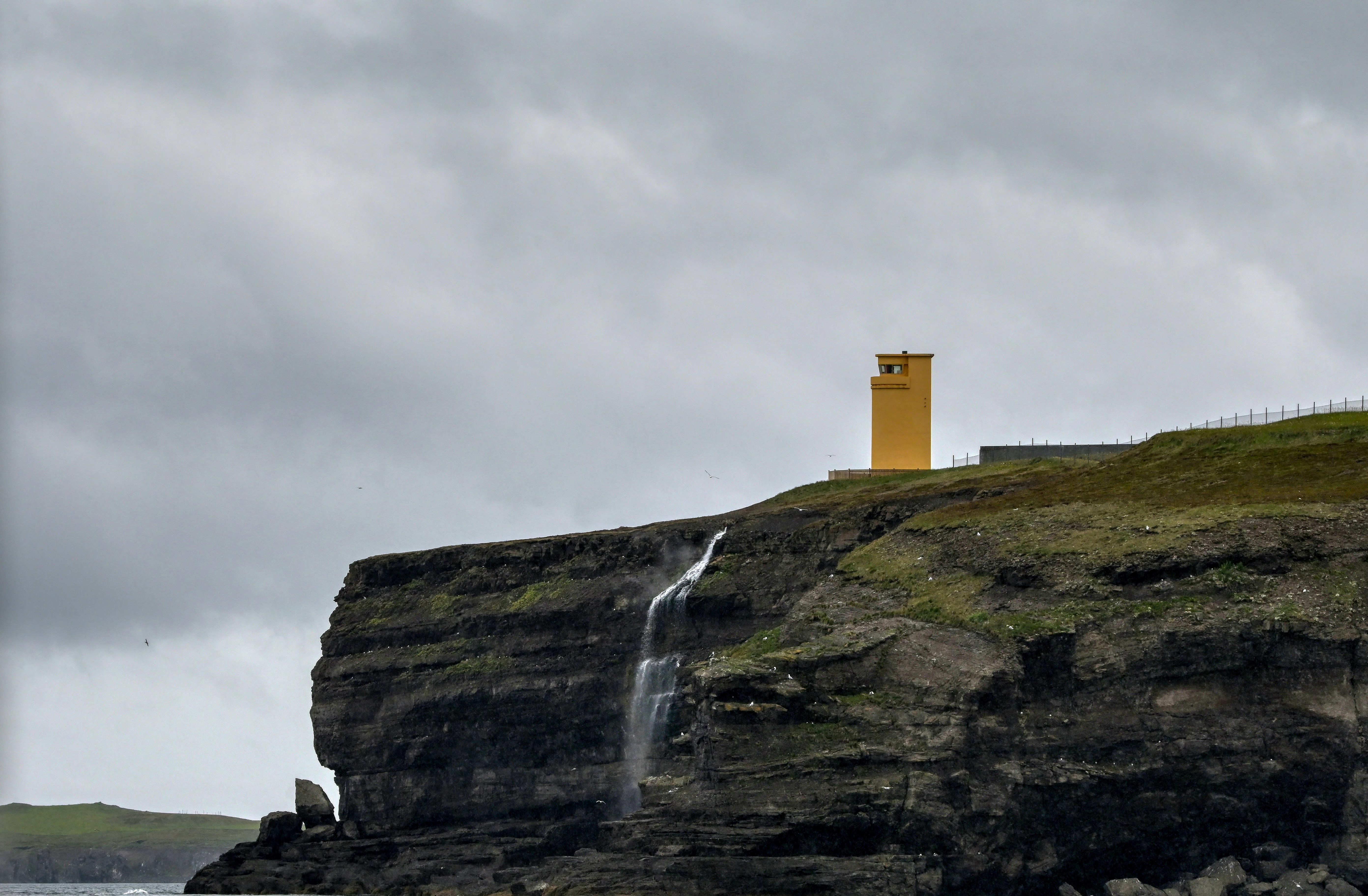 Yellow Beacon Crowns a Cliffside Vista Over a Narrow Waterfall