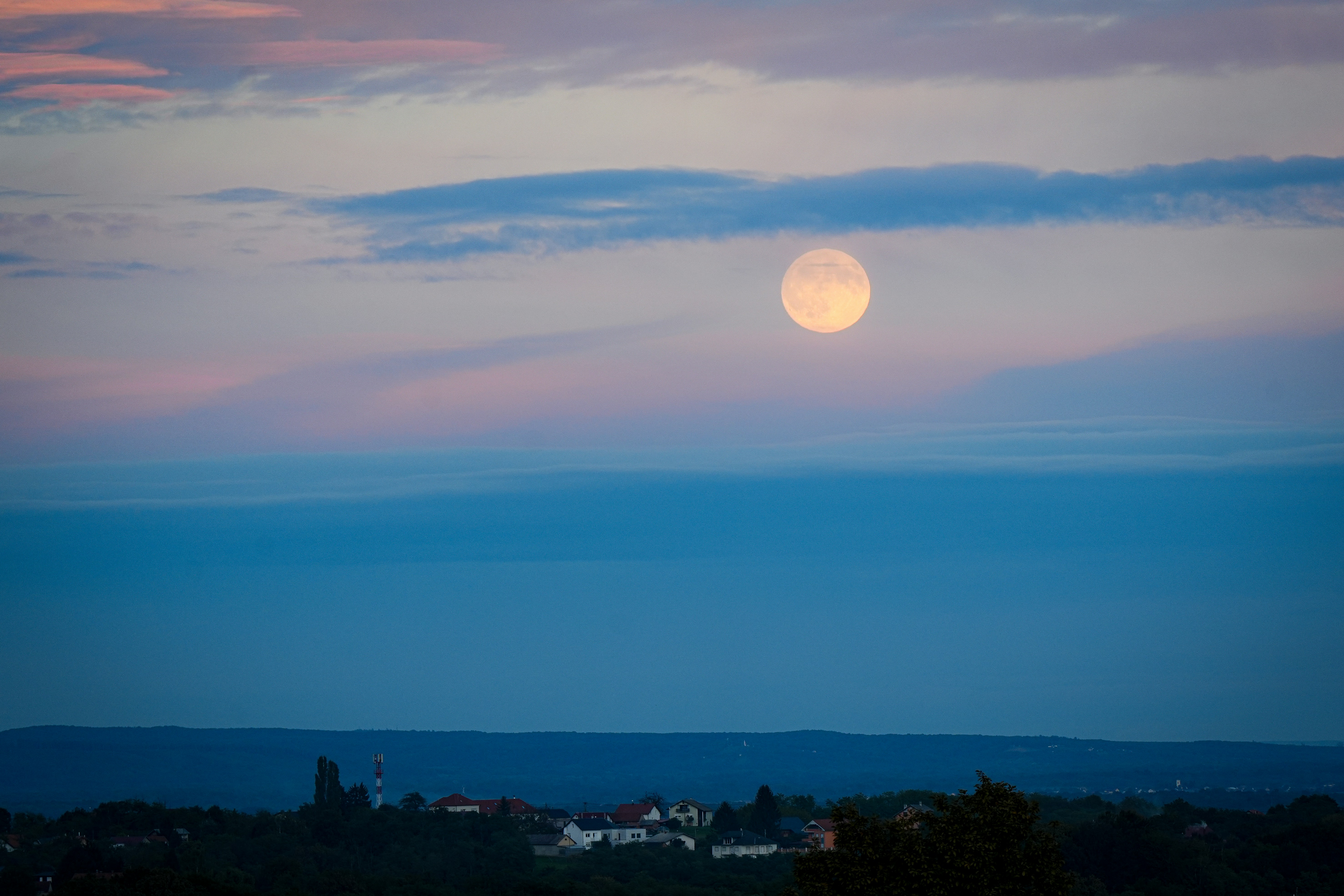 Full moon rising over a distant landscape at dusk.Nikola  Tomašić