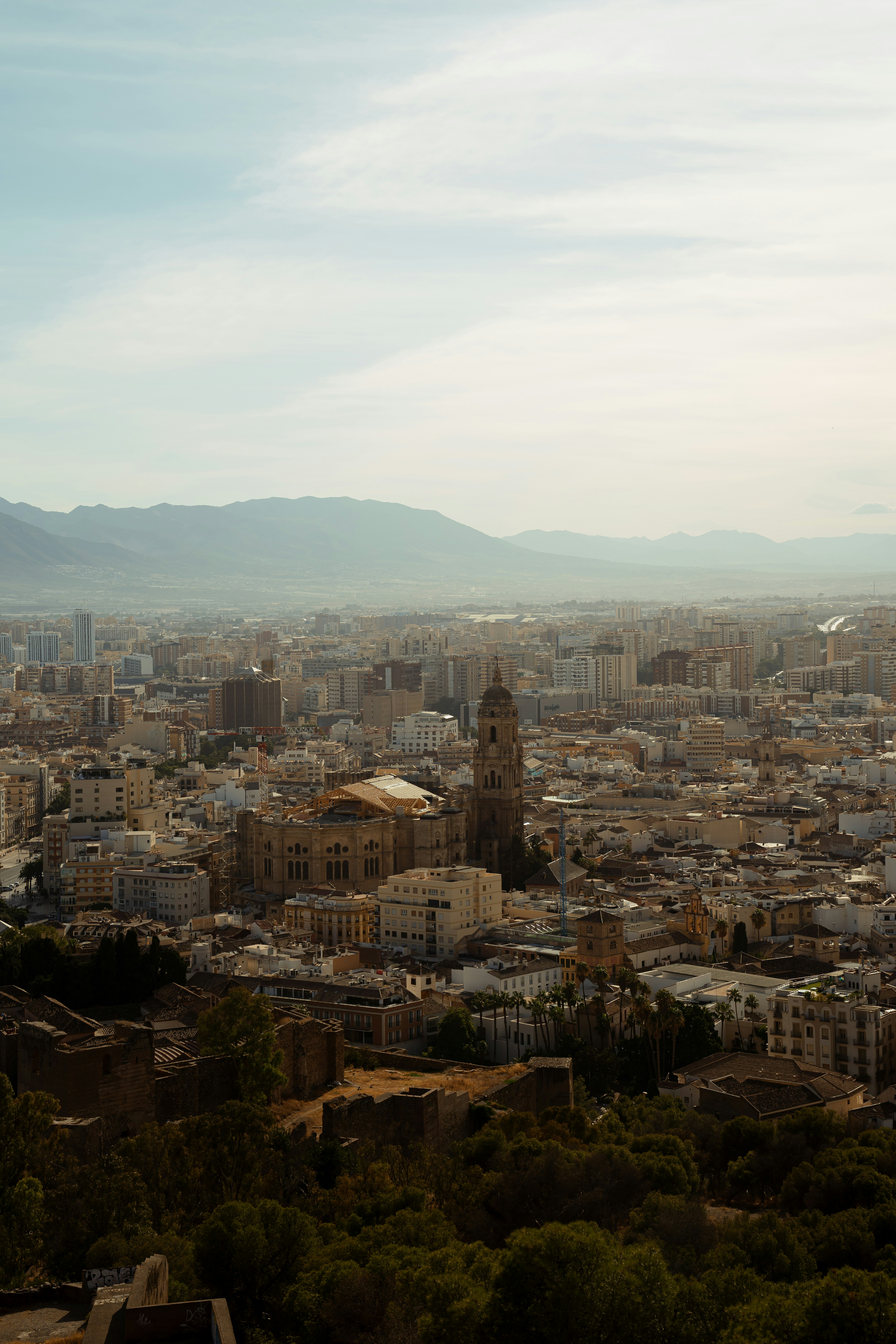 A panoramic view of a sprawling cityscape with historical architecture nestled among modern buildings, framed by distant mountains. The scene captures the essence of urban life and natural beauty.