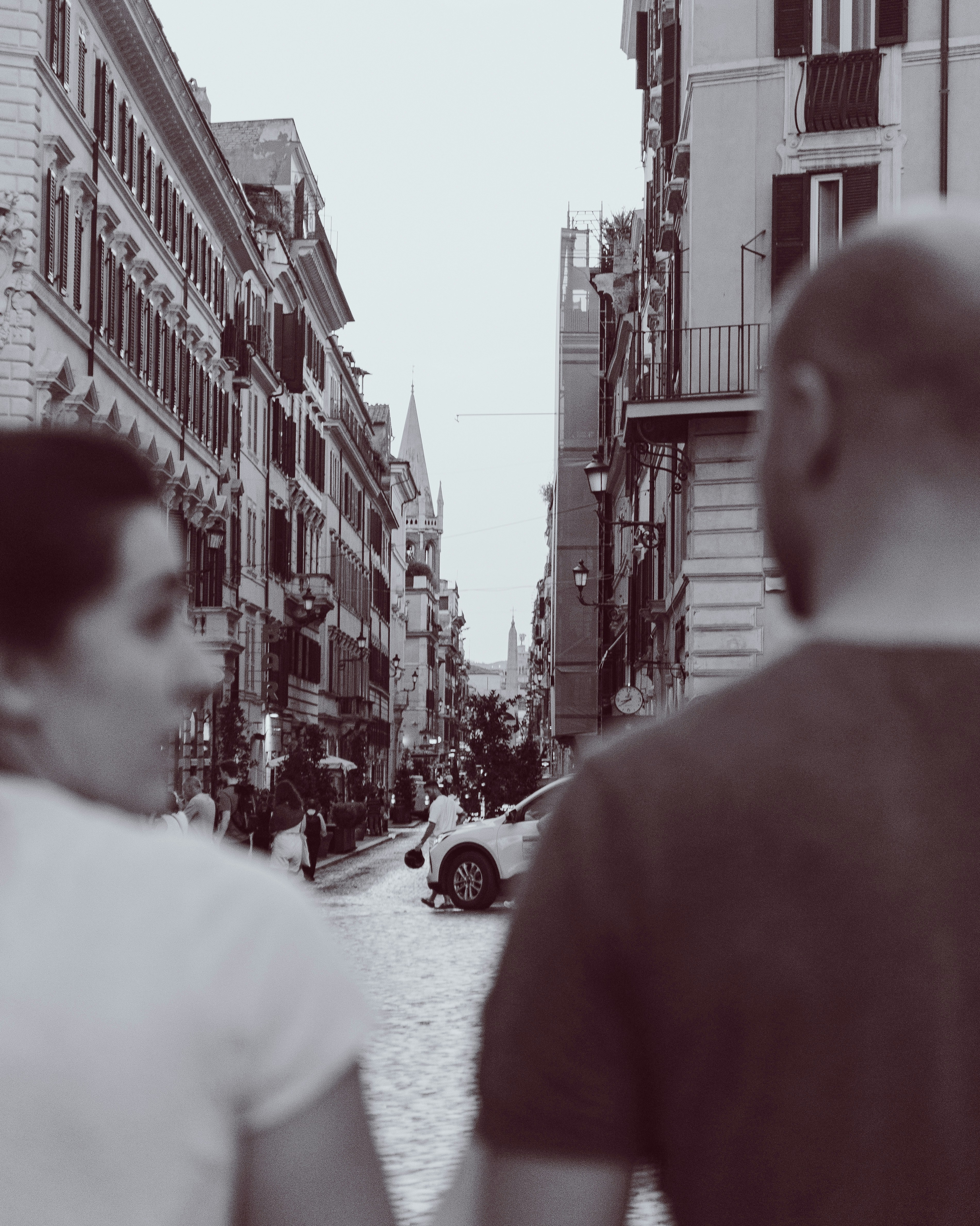 Couple walking hand-in-hand through a bustling cobblestone street, framed by historic architecture and a distant church spire.