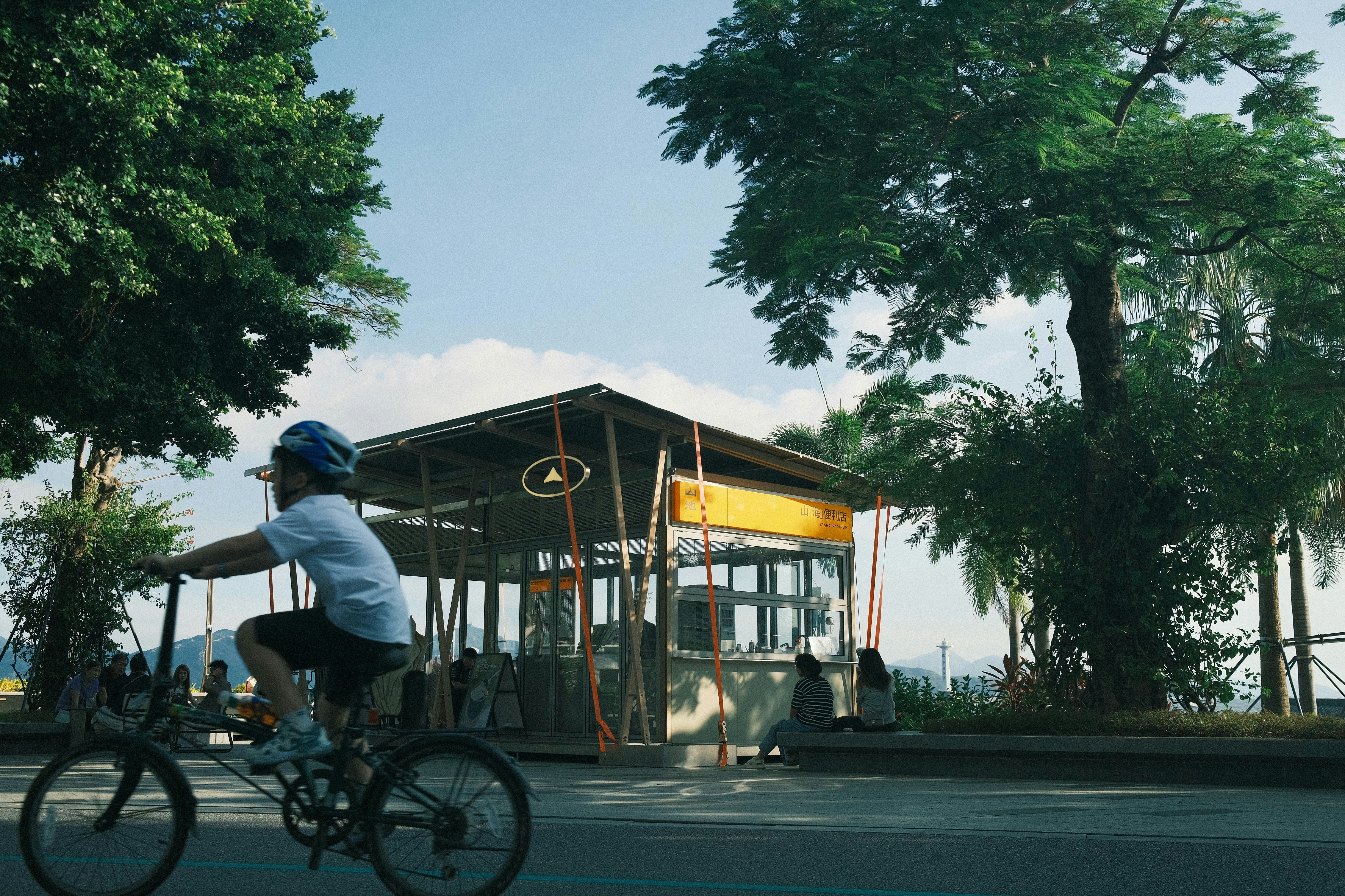 Person riding a bicycle past a small building.