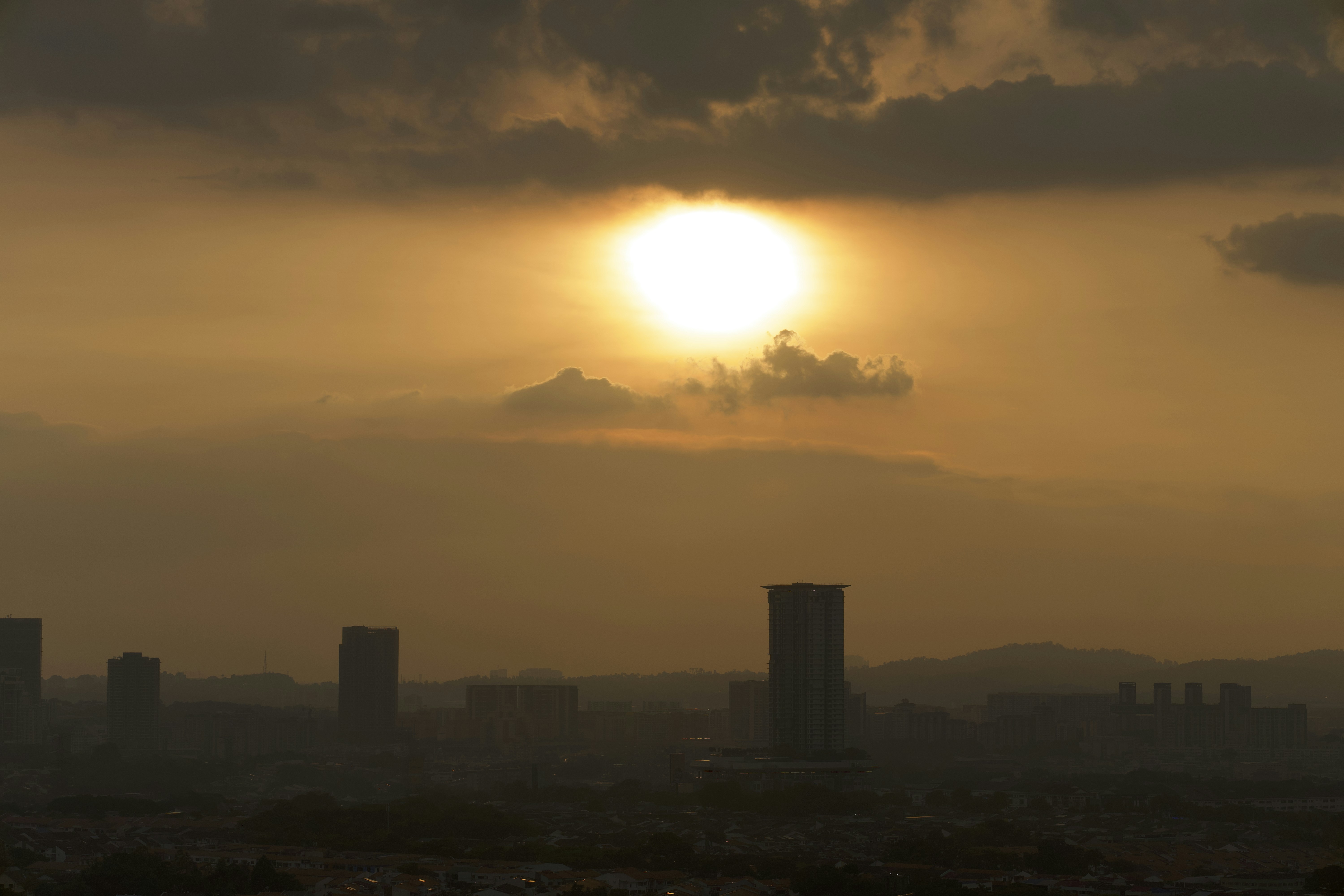 Sun setting over a hazy cityscape with silhouetted buildings.