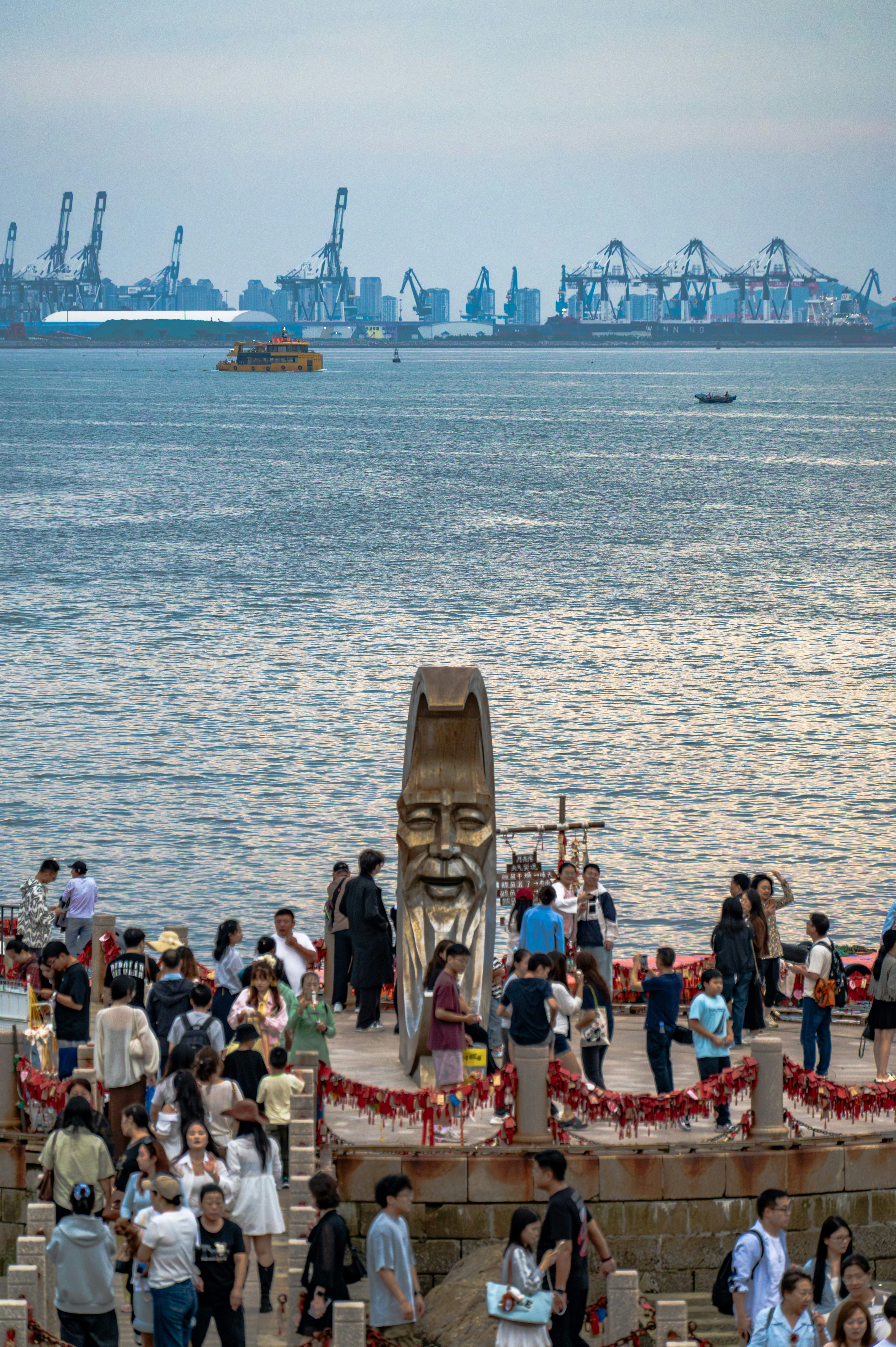 People gather by the water near a large statue.
