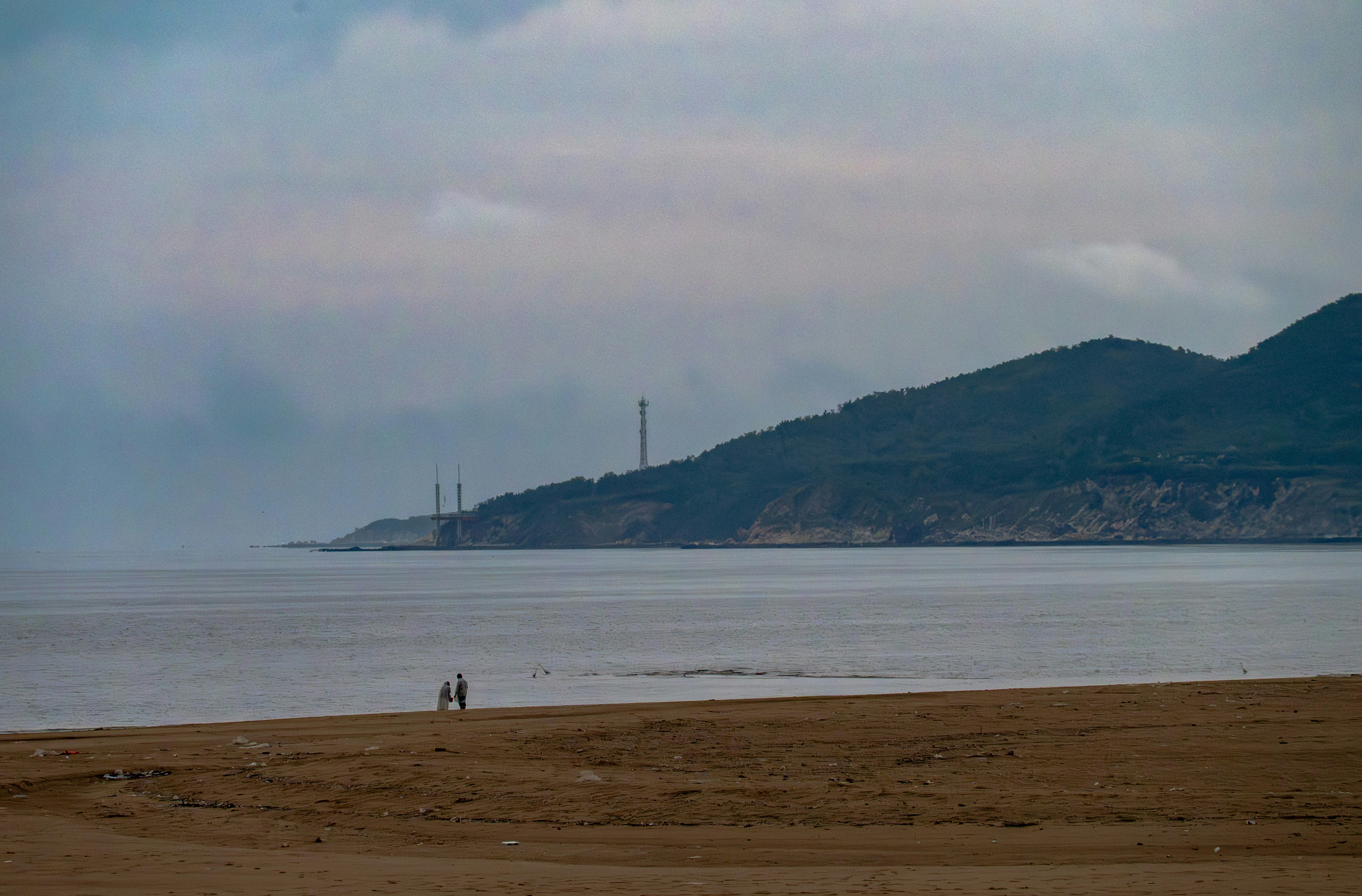 Two people walk on a sandy beach by the ocean.