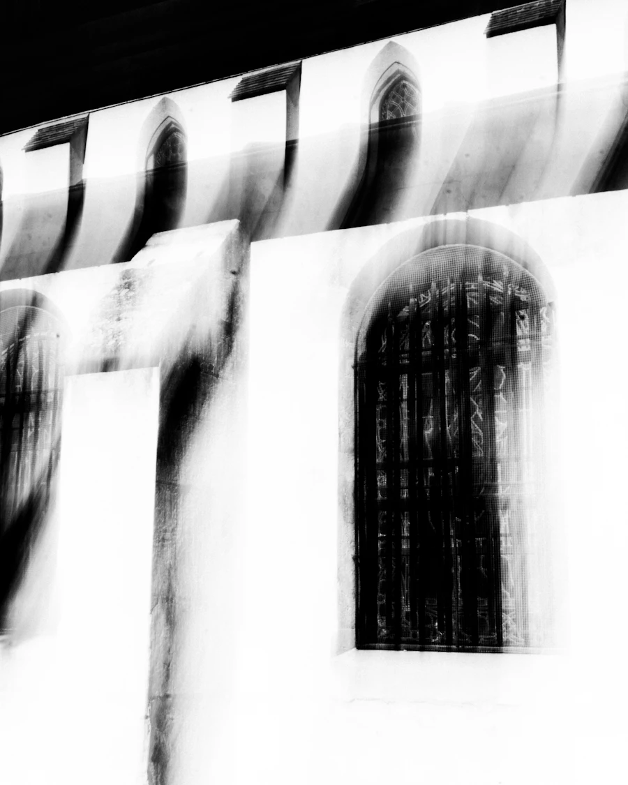 High-contrast black-and-white view of a building facade with arched windows and motion blur streaking across the frame. The largest dark window on the right anchors the composition.
