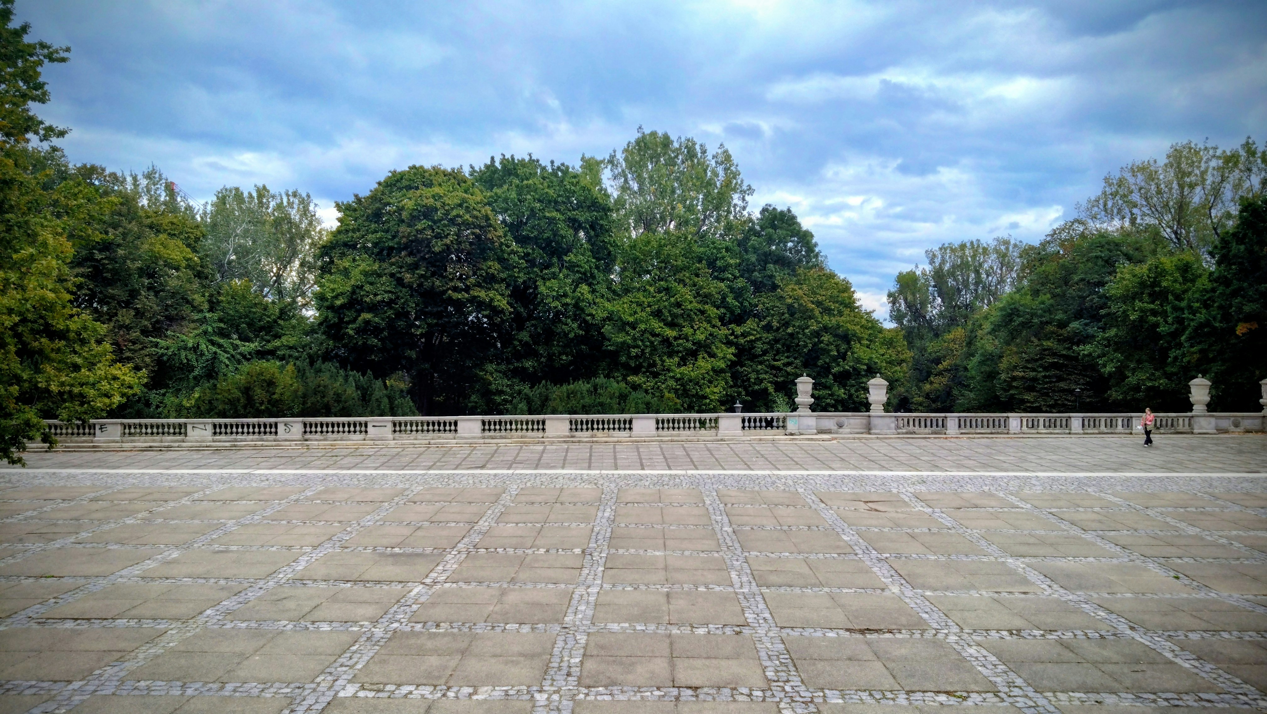 Paved plaza with trees and cloudy sky