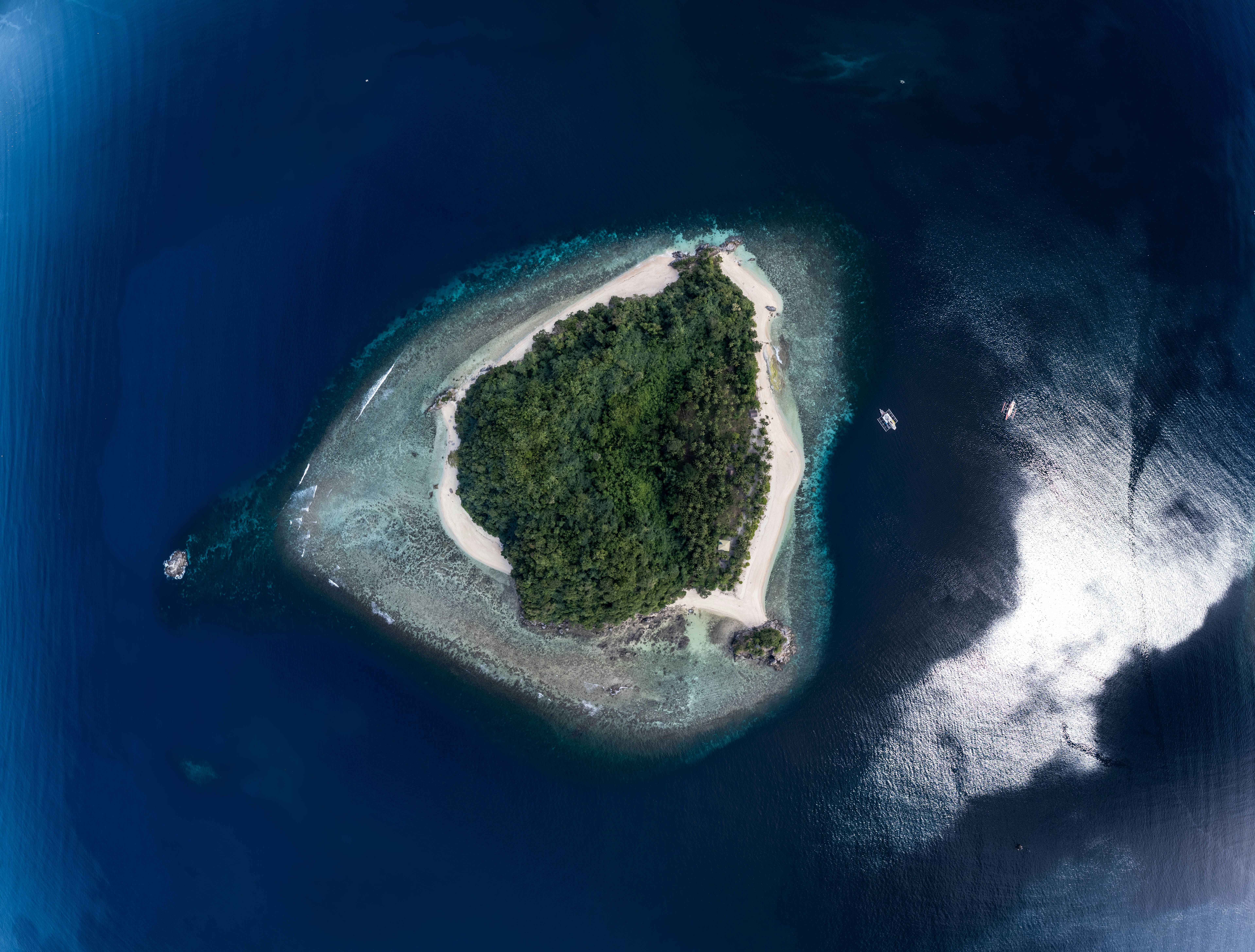 Aerial view of a lush, green island surrounded by vibrant blue waters, showcasing a pristine beach and coral reefs. The scene conveys a sense of tranquility and natural beauty.