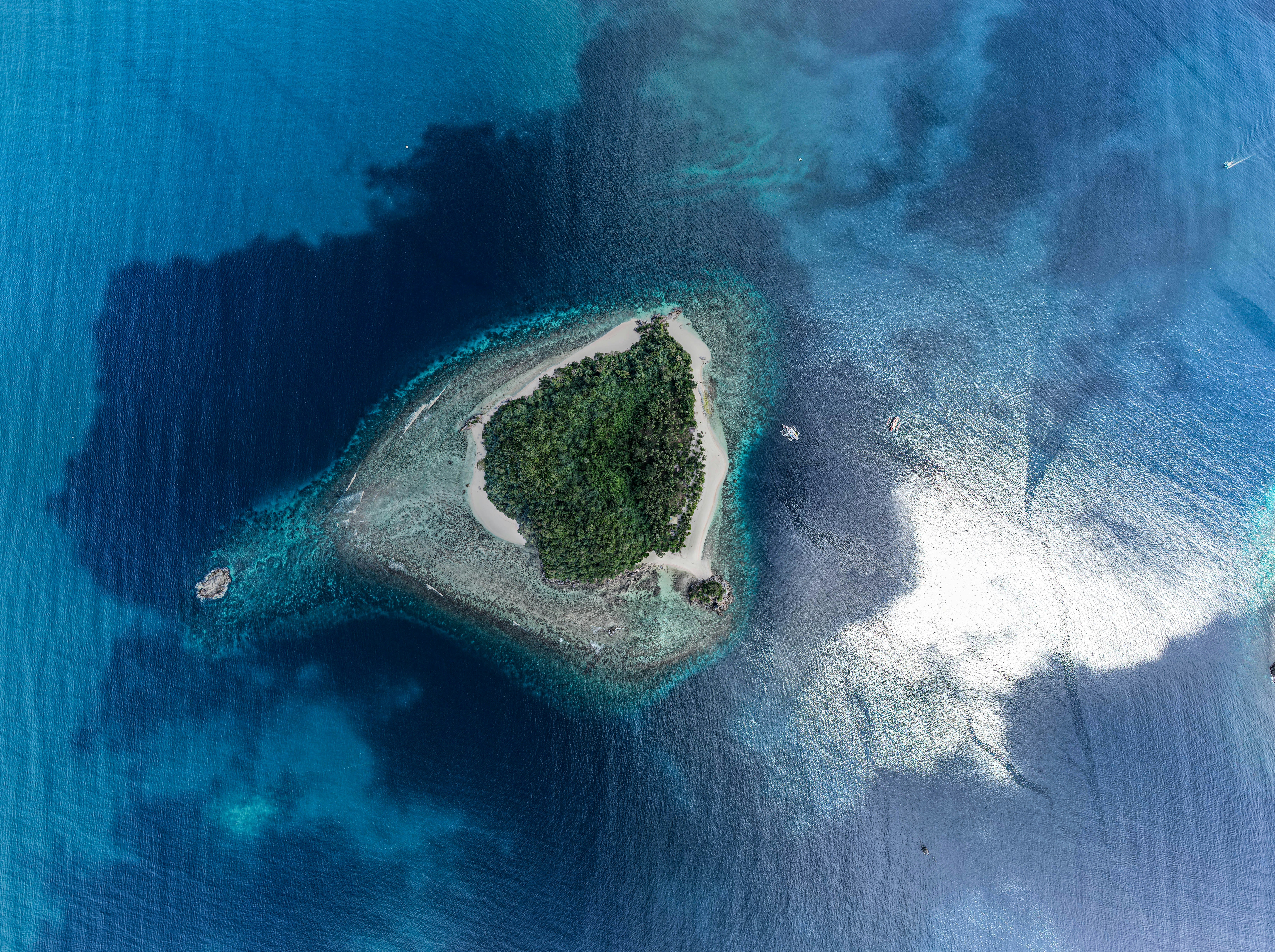 Aerial view of a small, lush island surrounded by vibrant blue waters and coral reefs, showcasing the natural beauty of coastal landscapes.