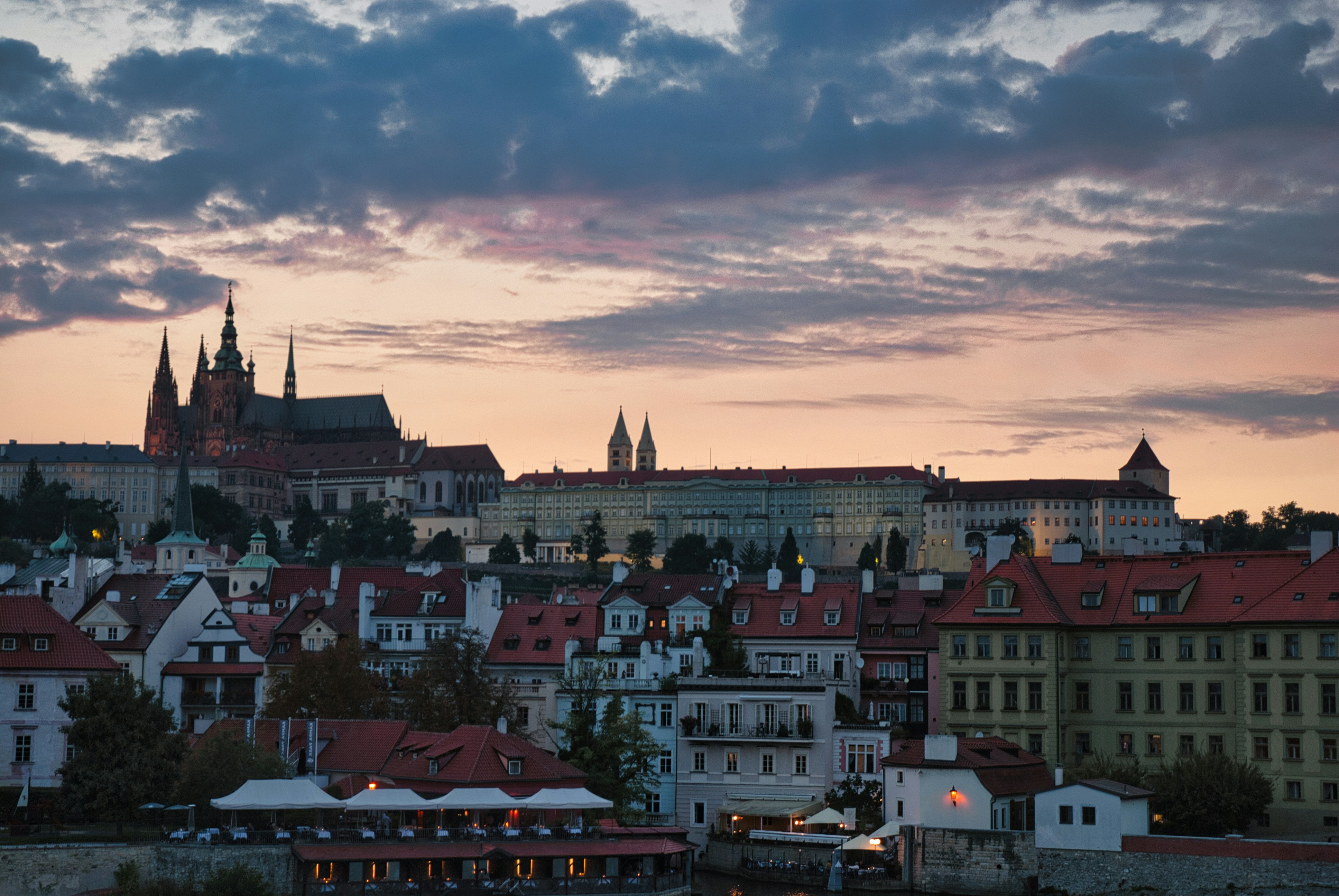 Historic skyline of Prague at twilight, featuring St. Vitus Cathedral and colorful rooftops along the Vltava River.