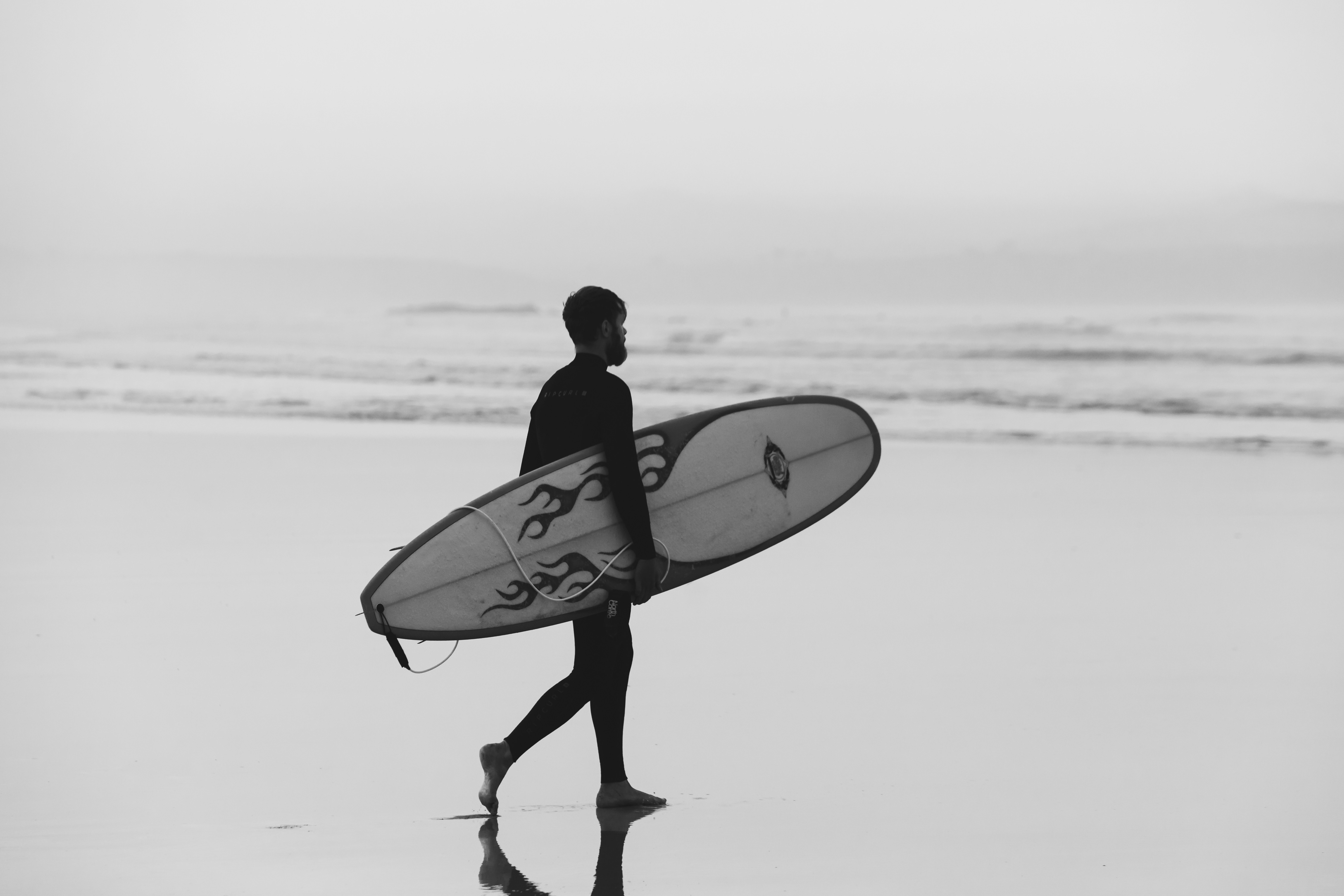 Reflections, Cornwall, UK | Man carrying surfboard walks on the beach.