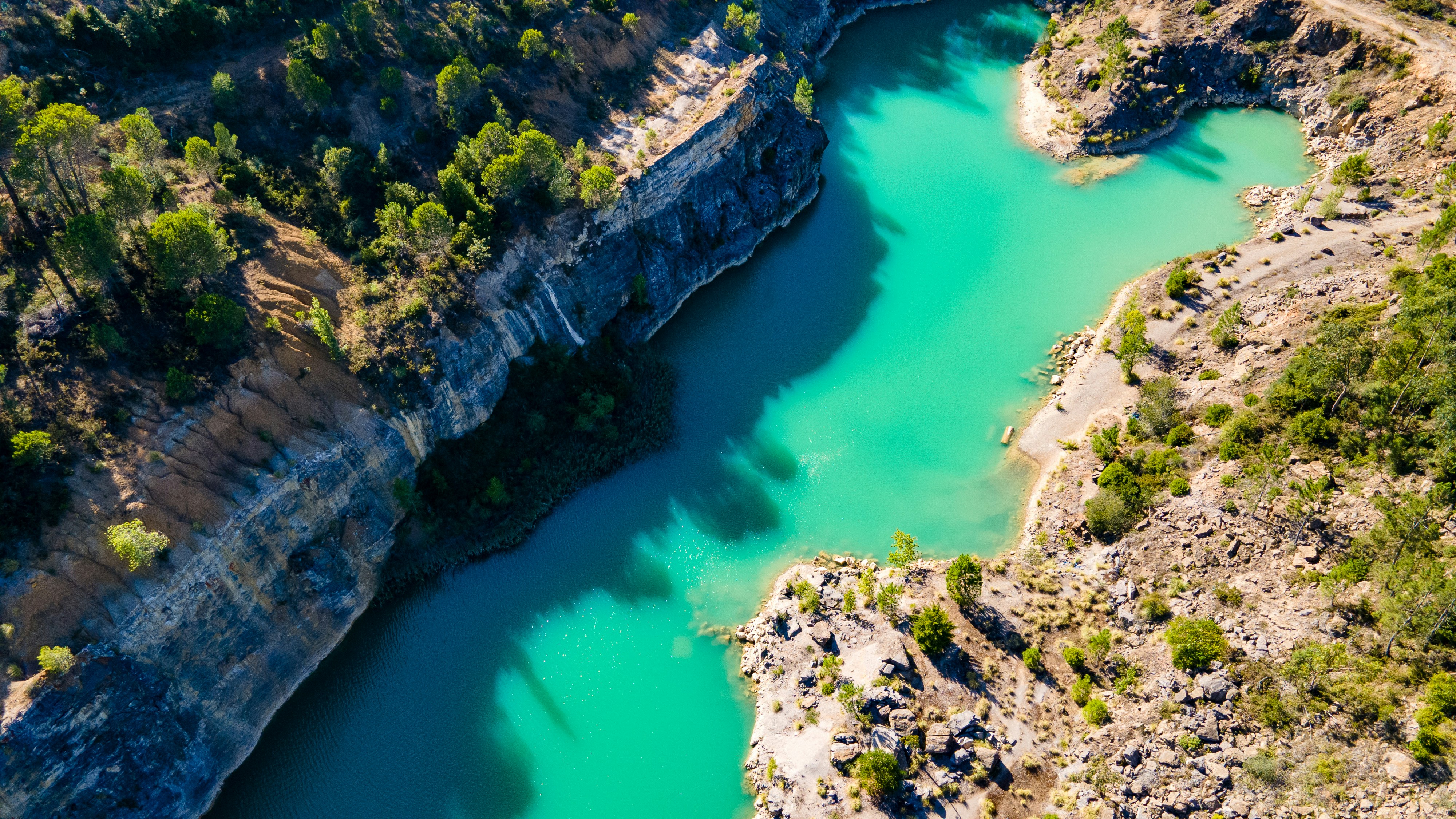 Aerial view of a vibrant turquoise river winding through rugged cliffs and lush greenery, highlighting the contrast between water and earth. The scene captures the natural beauty of the landscape.