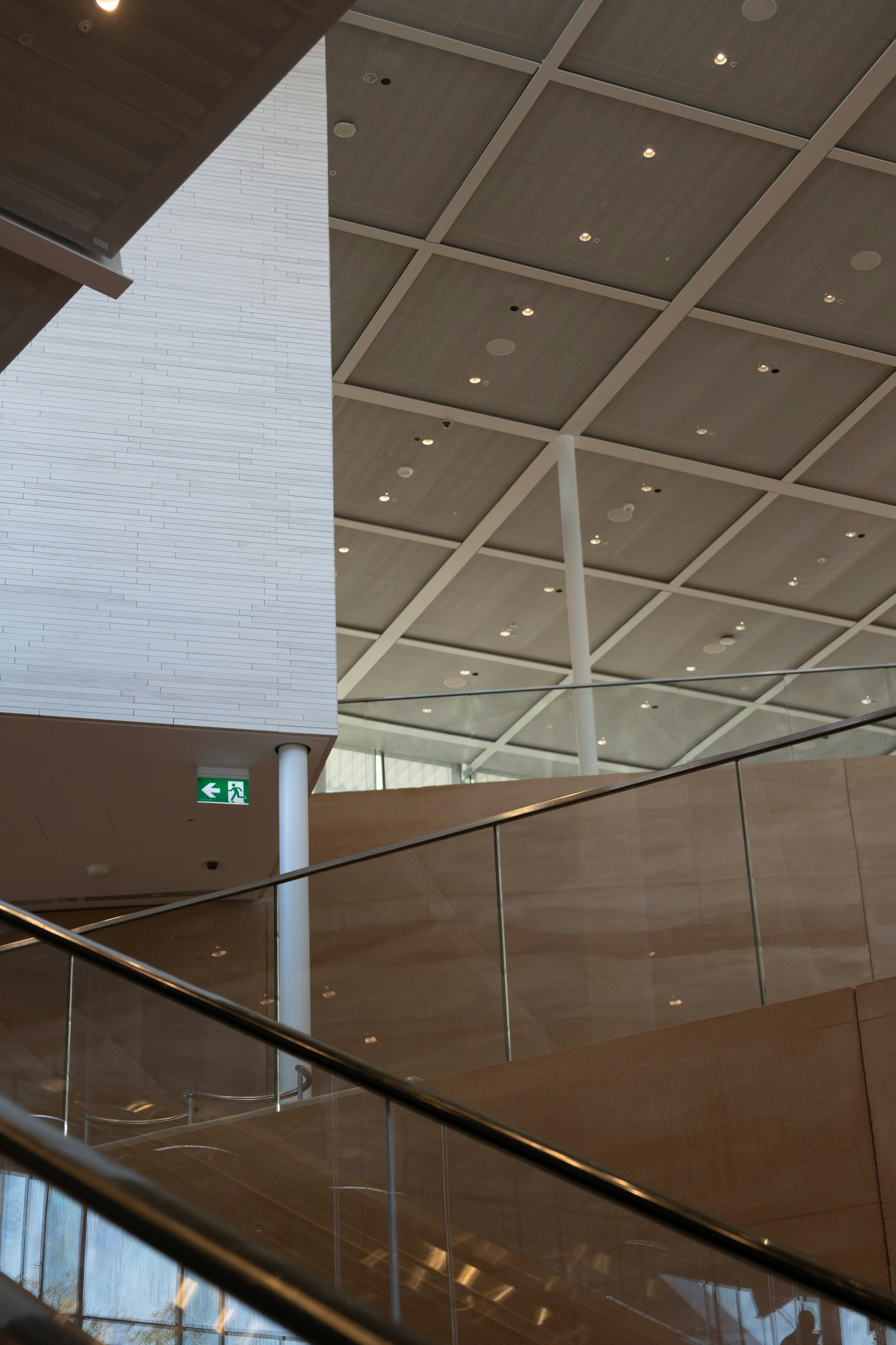 A minimalist interior featuring a glass railing, geometric ceiling panels, and soft natural light. Captures clean lines and contemporary design—ideal for architecture, modern interiors, and public space themes. | Modern interior with escalator and geometric ceiling
