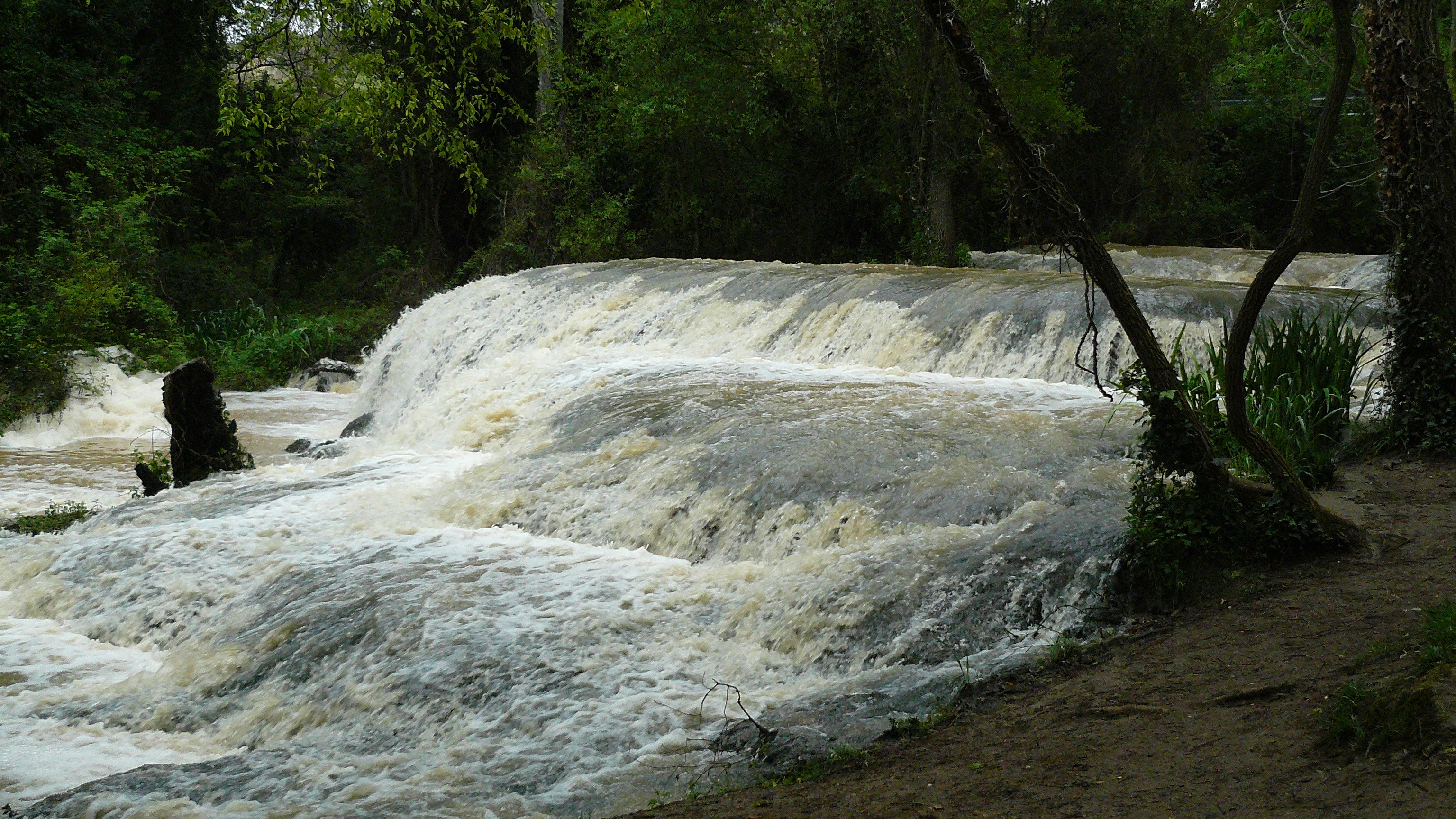 A wide, gentle waterfall flows over rocks.