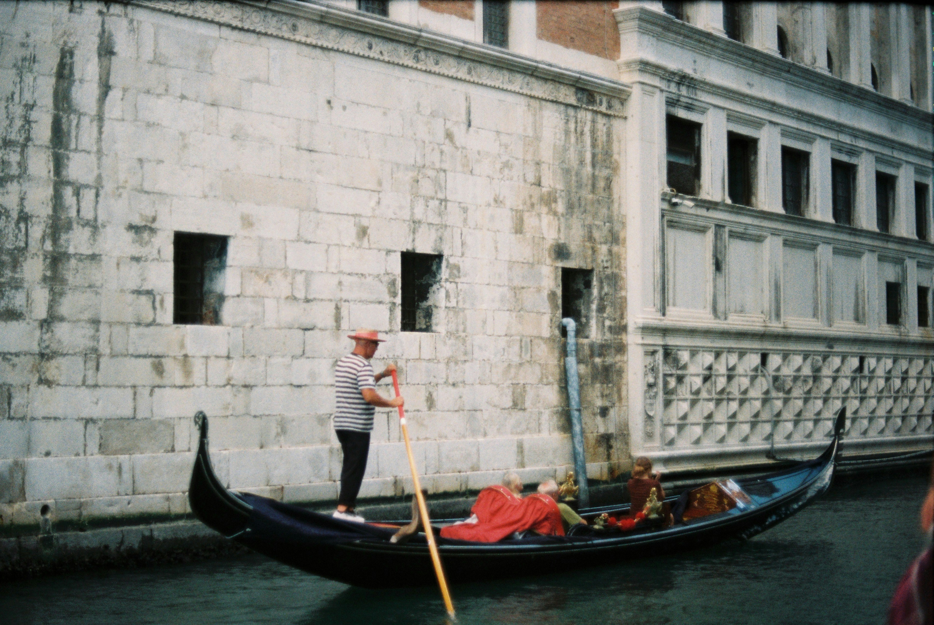Gondolier steers boat with passengers past building.