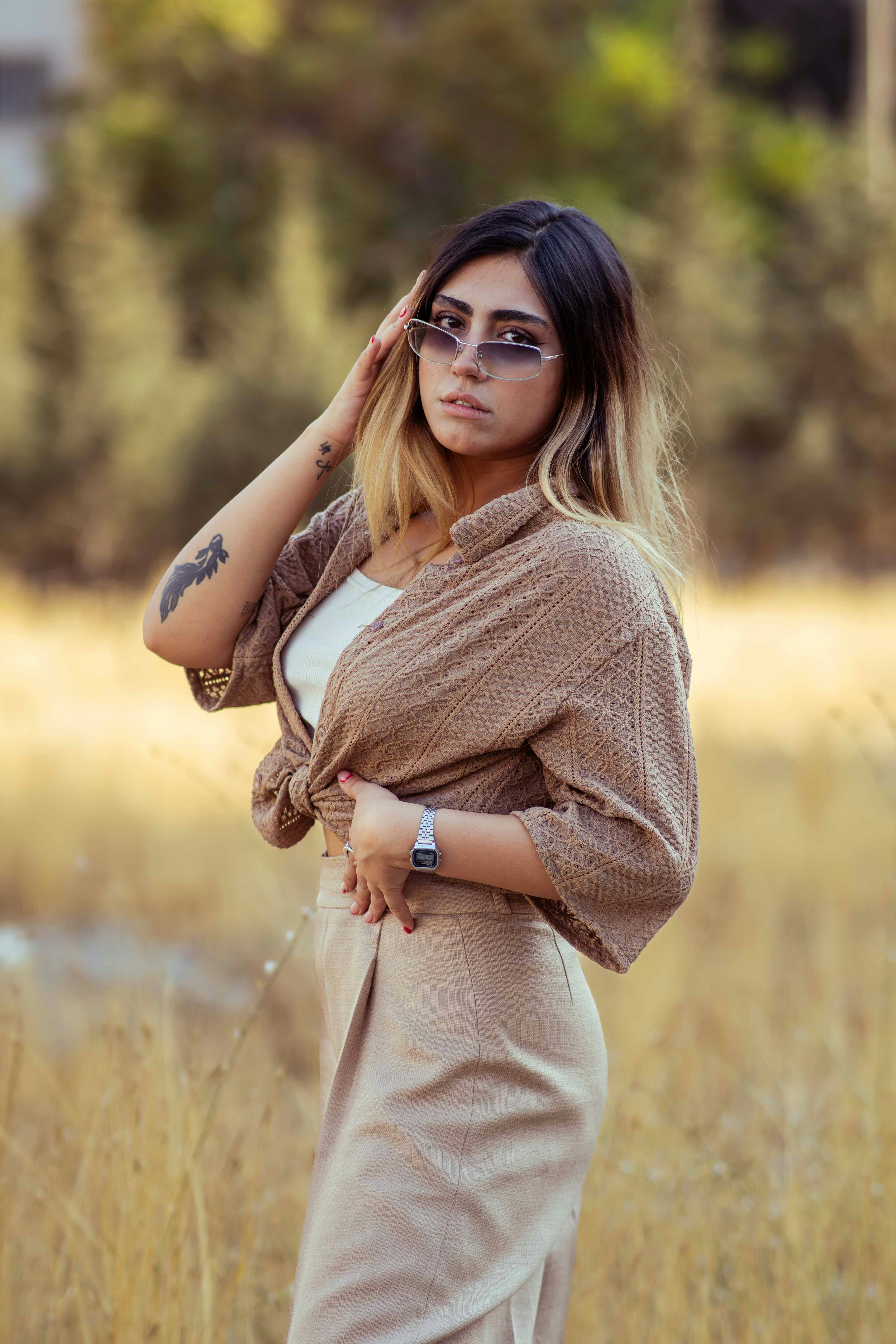 A woman in a stylish outfit poses gracefully amidst golden grasses, showcasing her fashion sense and confidence.