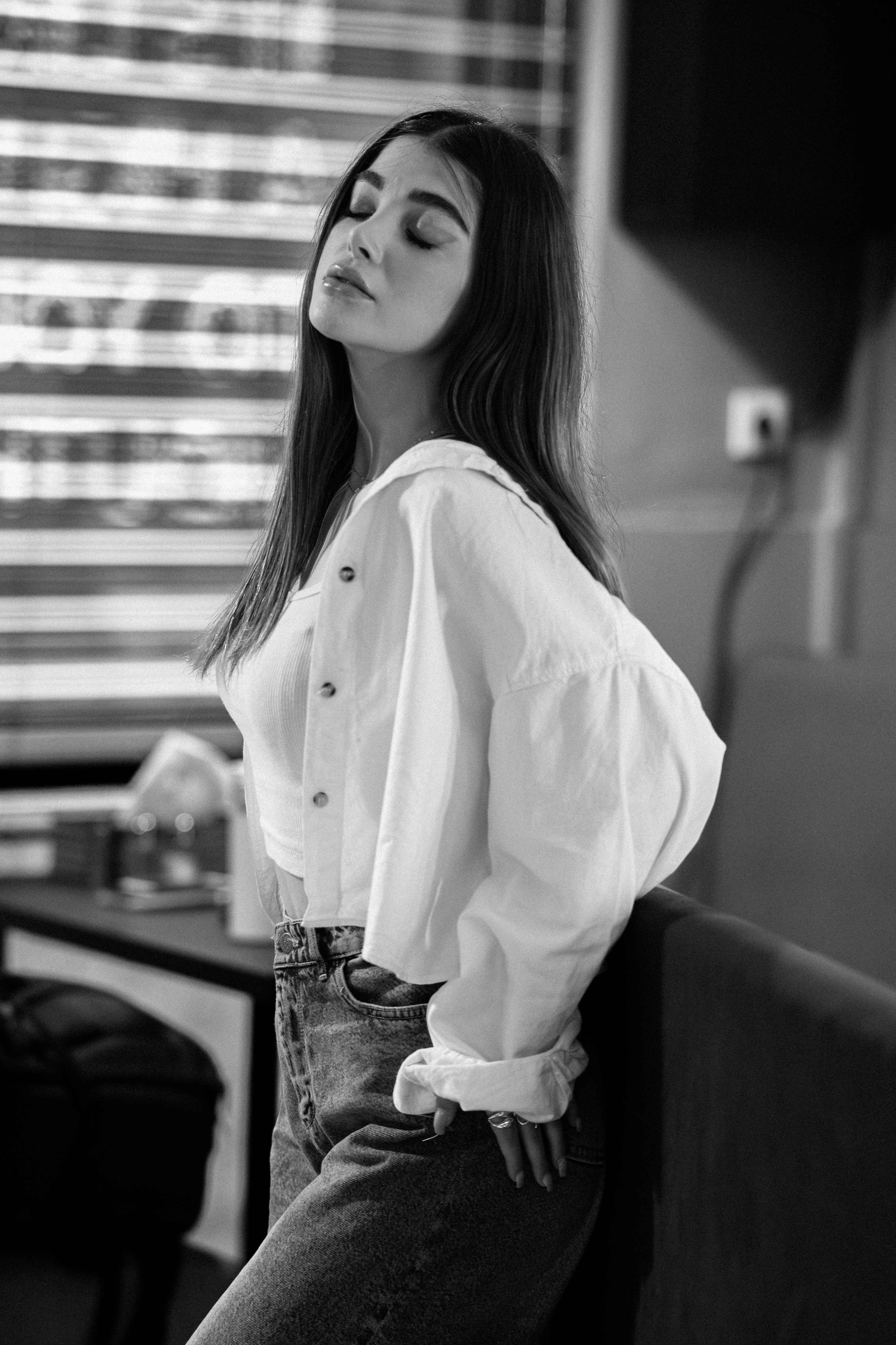 A young woman poses gracefully against a backdrop of soft lines and shadows, exuding a serene charm in monochrome.