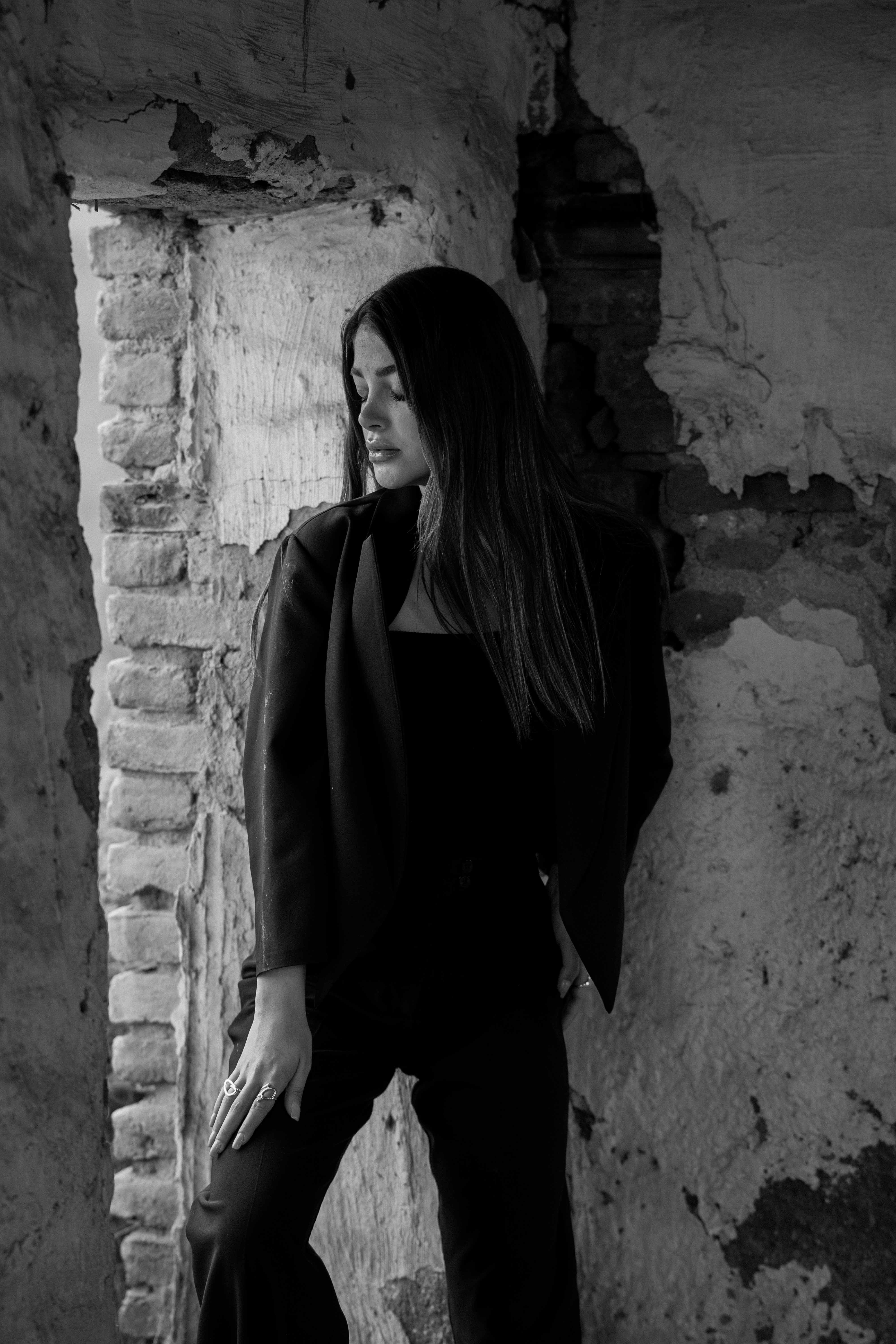 Woman in black suit standing near weathered wall