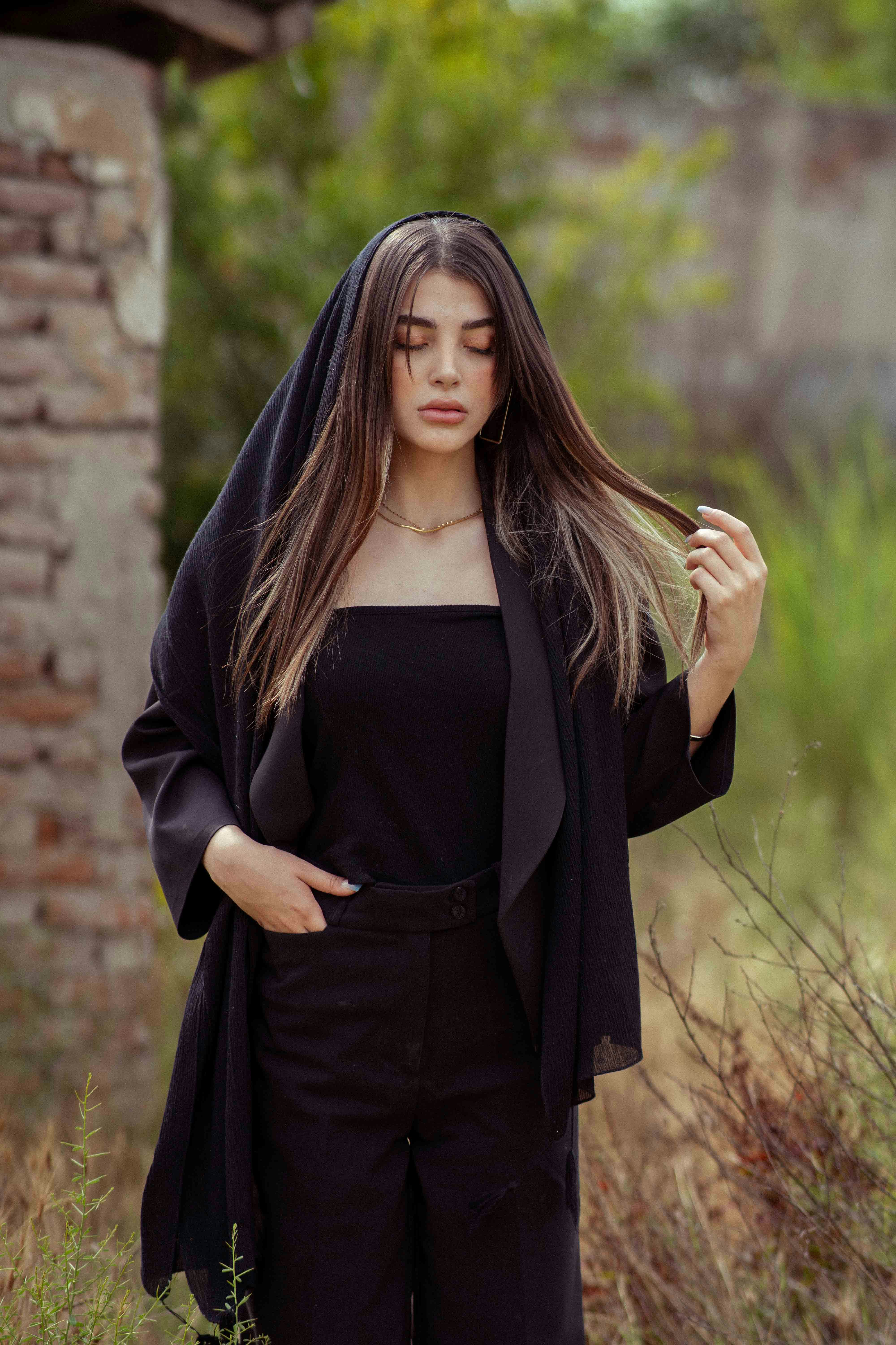 A young woman in a black outfit stands gracefully in a natural setting, her long hair flowing as she interacts with her surroundings.