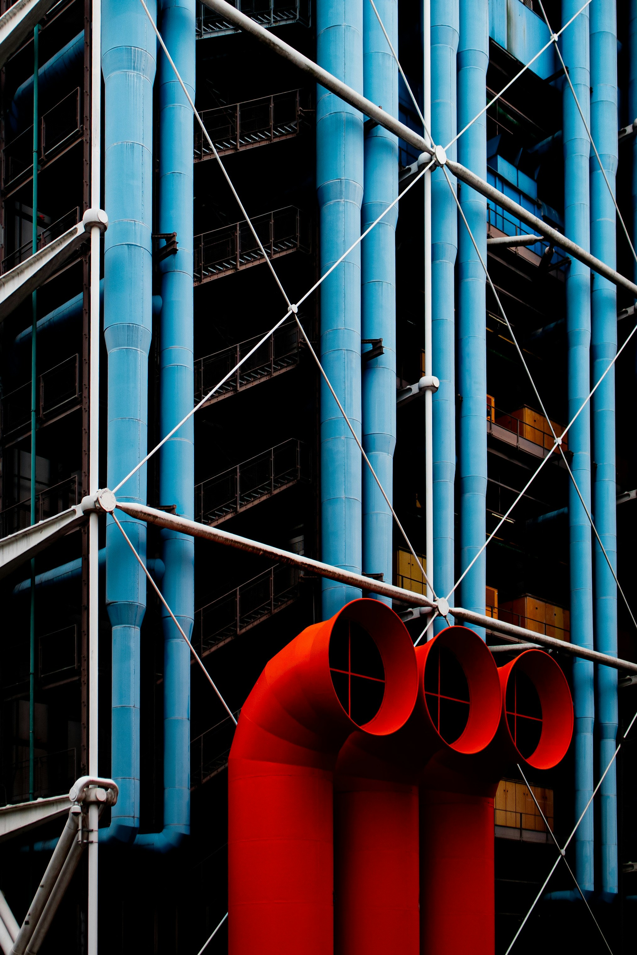 Vibrant blue and red industrial pipes contrast against a dark backdrop, showcasing modern architectural design elements. The image emphasizes geometric lines and shapes.