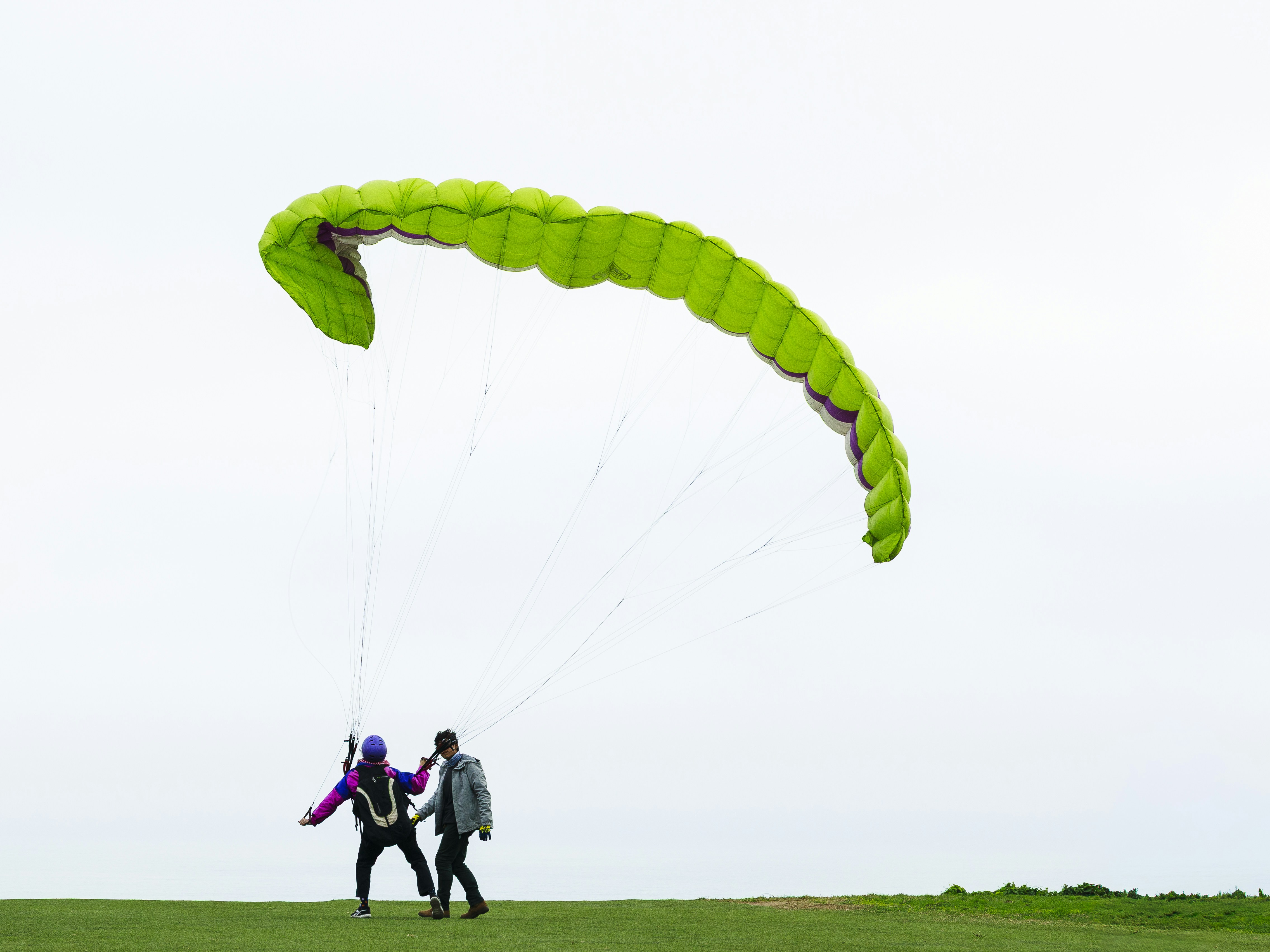 Two people preparing to paraglide on a grassy hill.