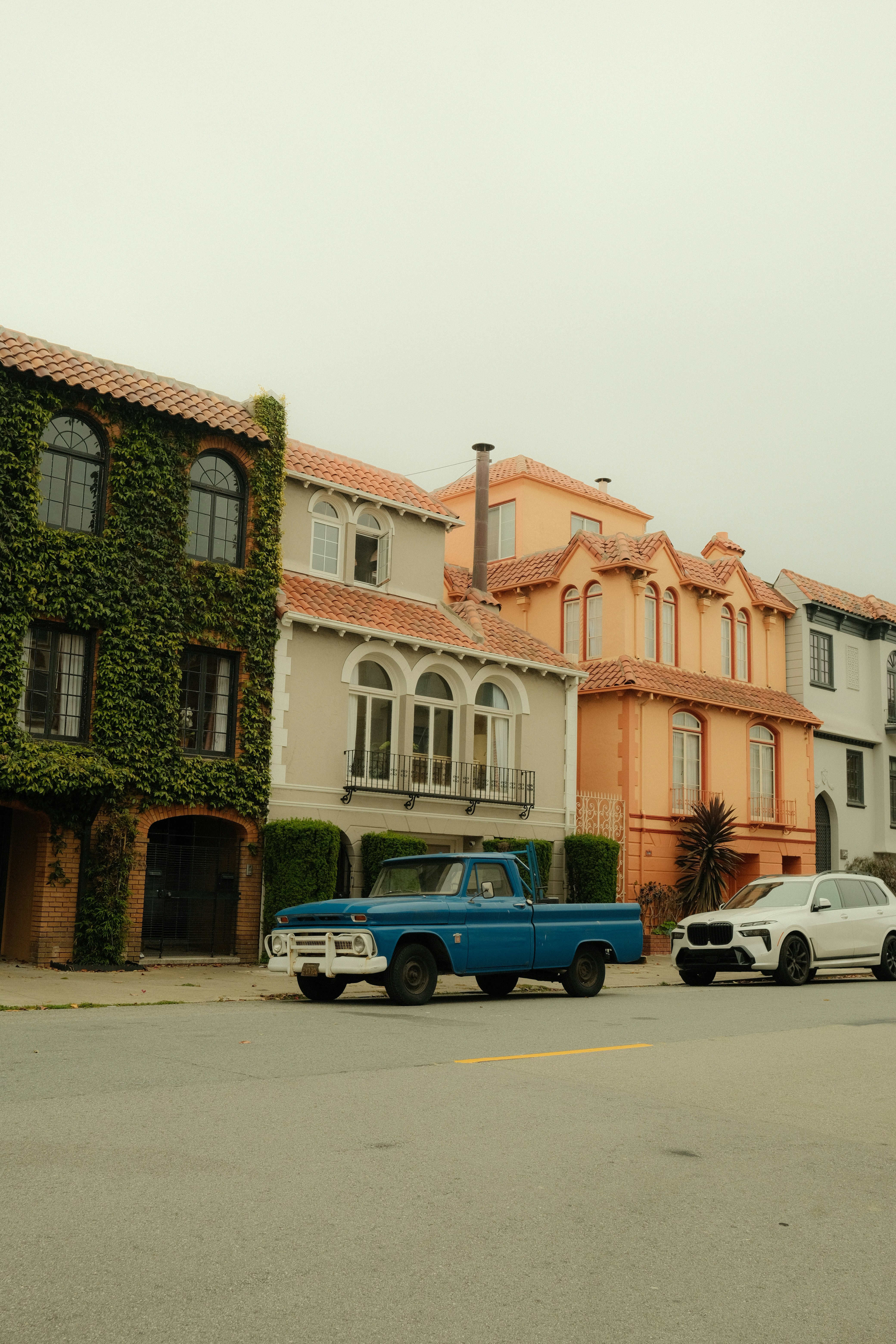 A vibrant blue vintage truck parked in front of eclectic houses adorned with greenery and colorful facades.