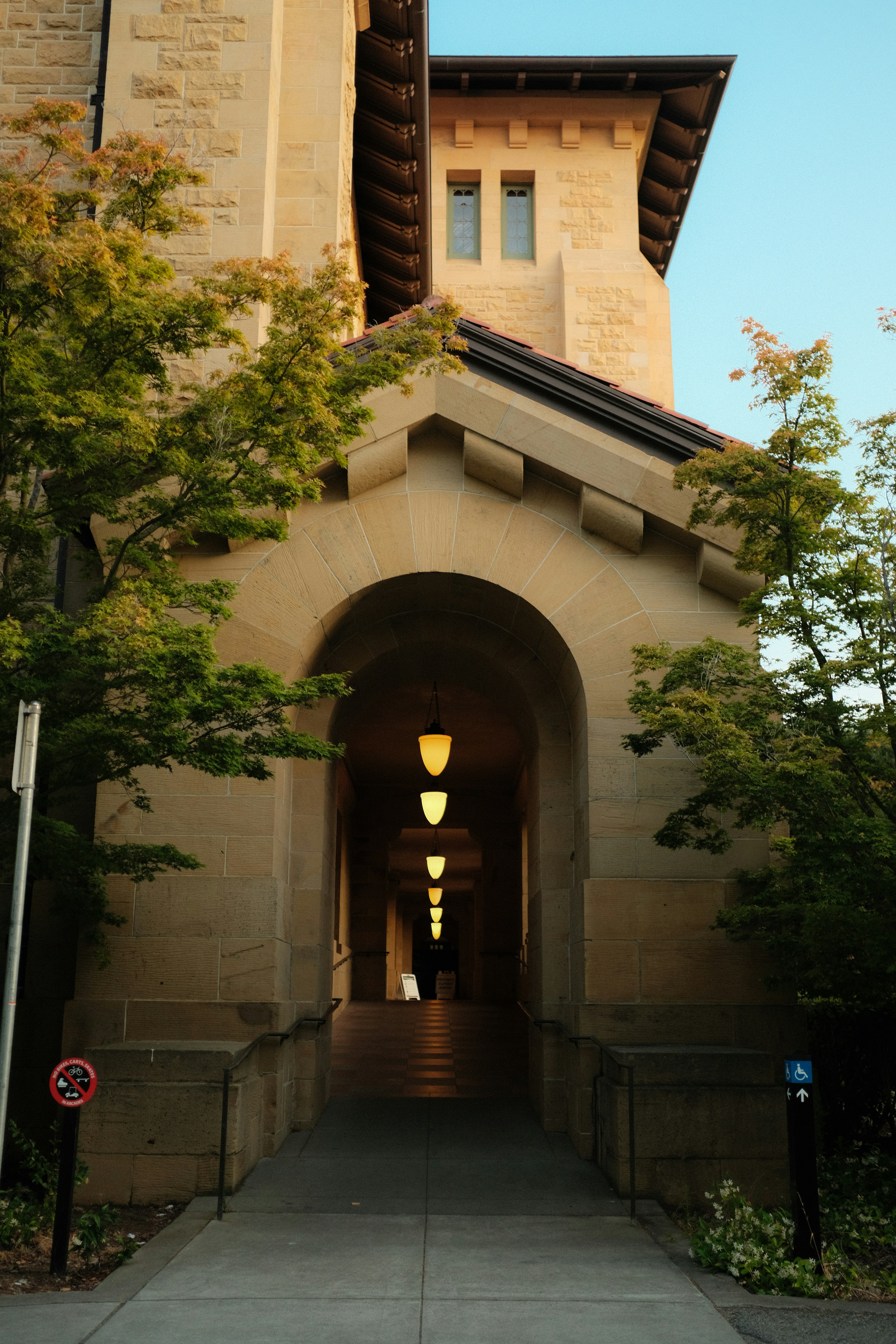 Stone archway framed by lush greenery, leading into a softly lit passageway. Warm lights illuminate the path ahead.
