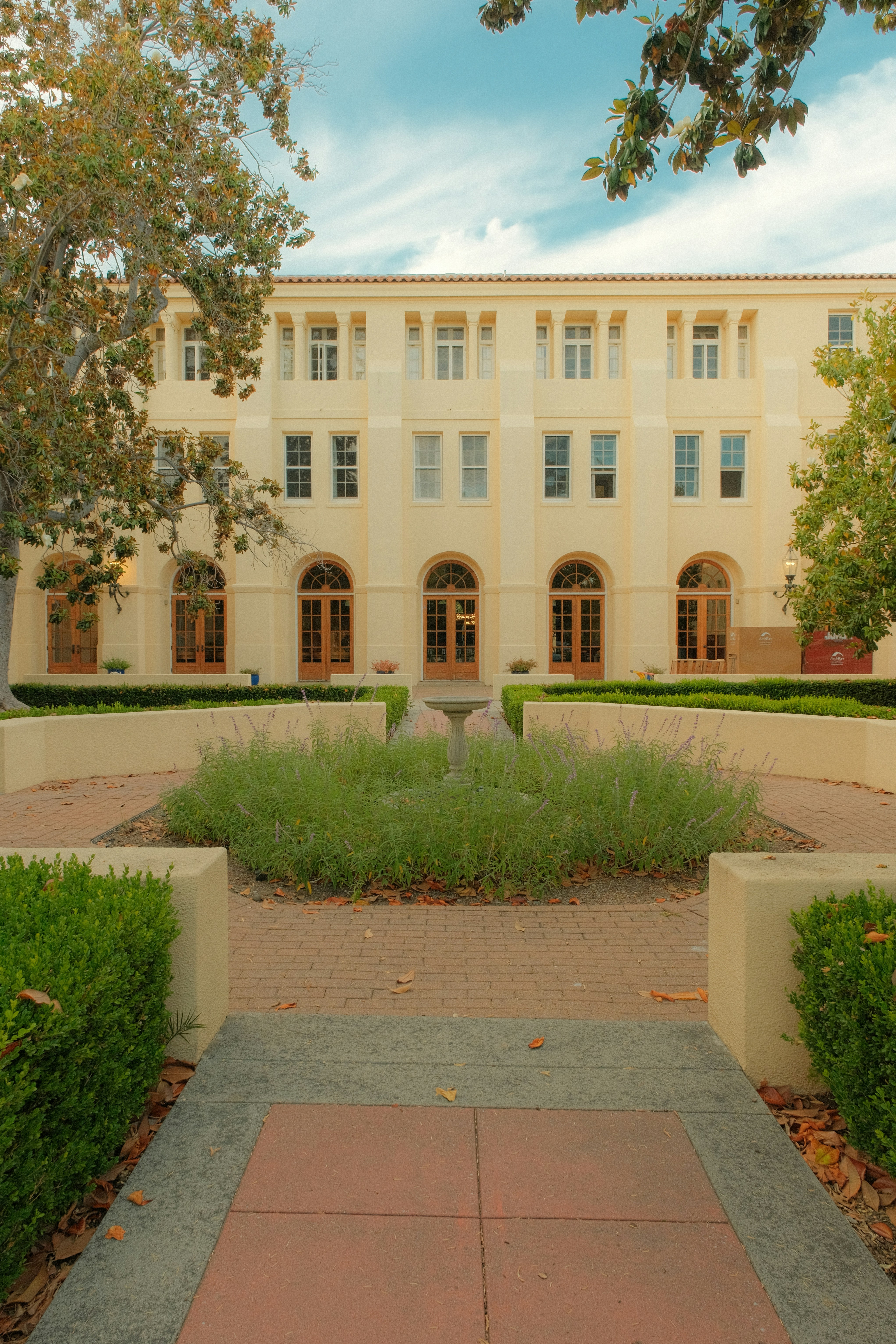 Elegant courtyard framed by lush greenery and classical architecture, showcasing a tranquil fountain at its center.
