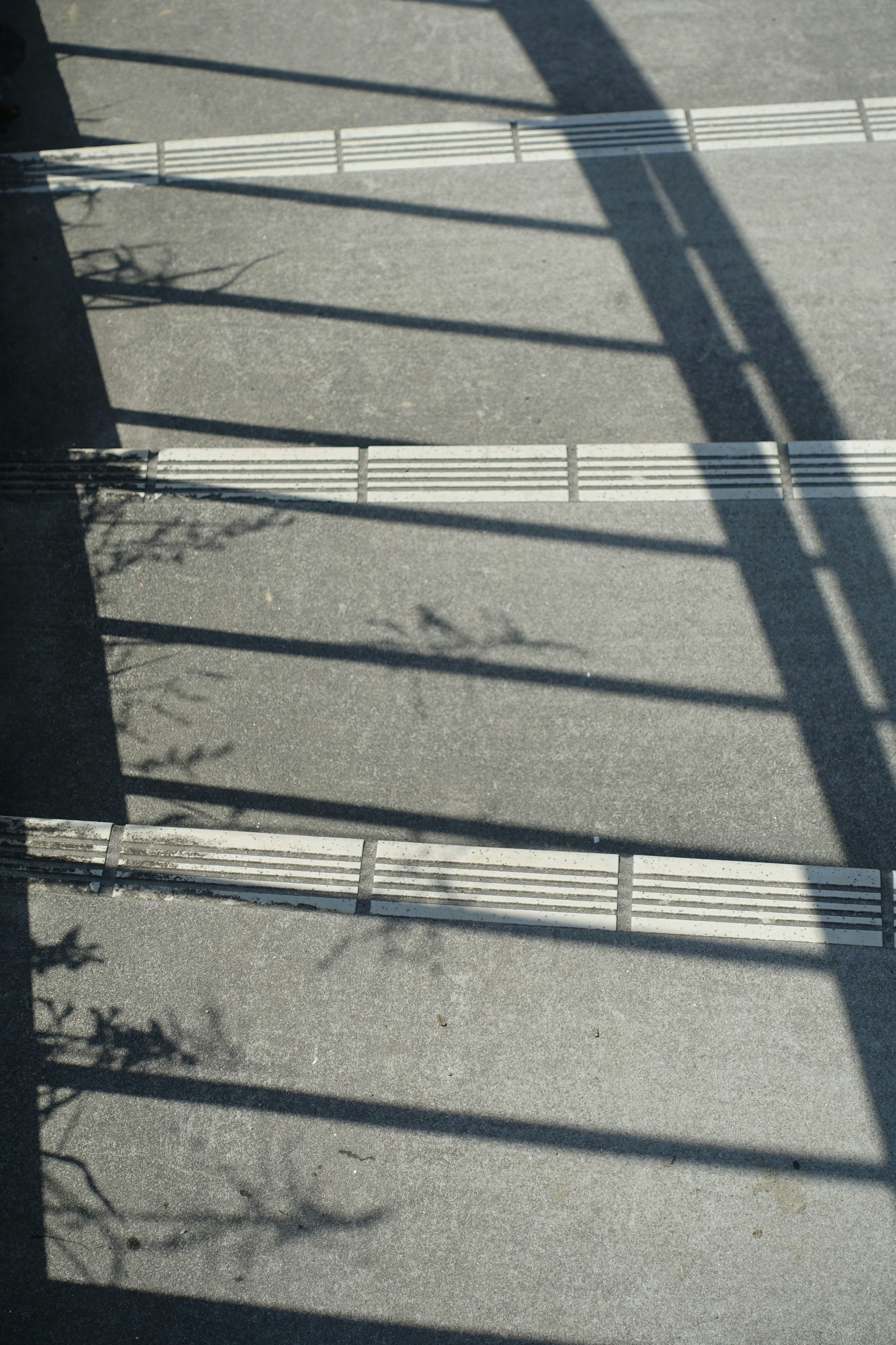 Intricate shadows cast by a railing create a dynamic pattern on the concrete surface, highlighting the interplay of light and architecture.