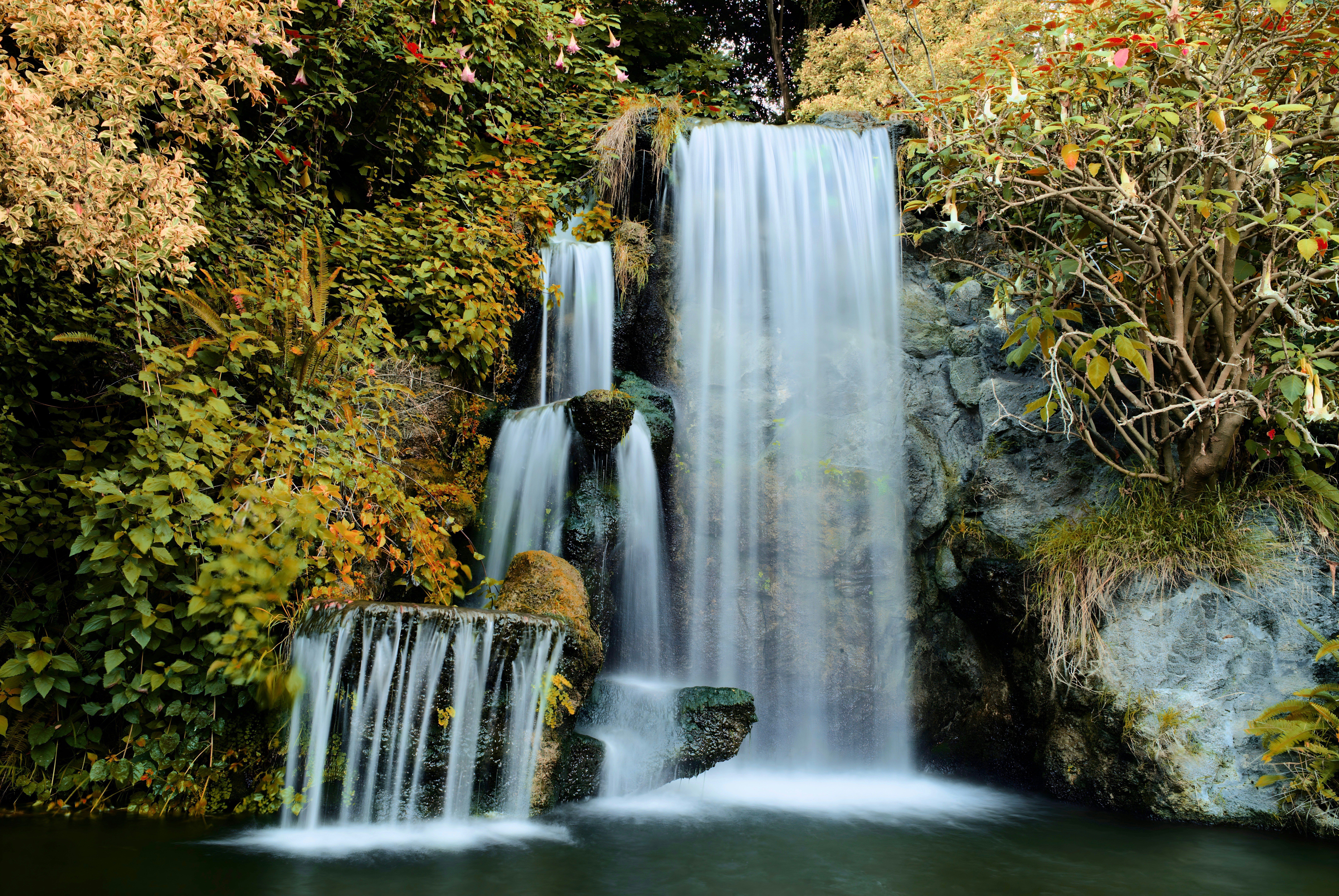 A tranquil waterfall flows gracefully over moss-covered rocks, surrounded by vibrant foliage in autumn hues.