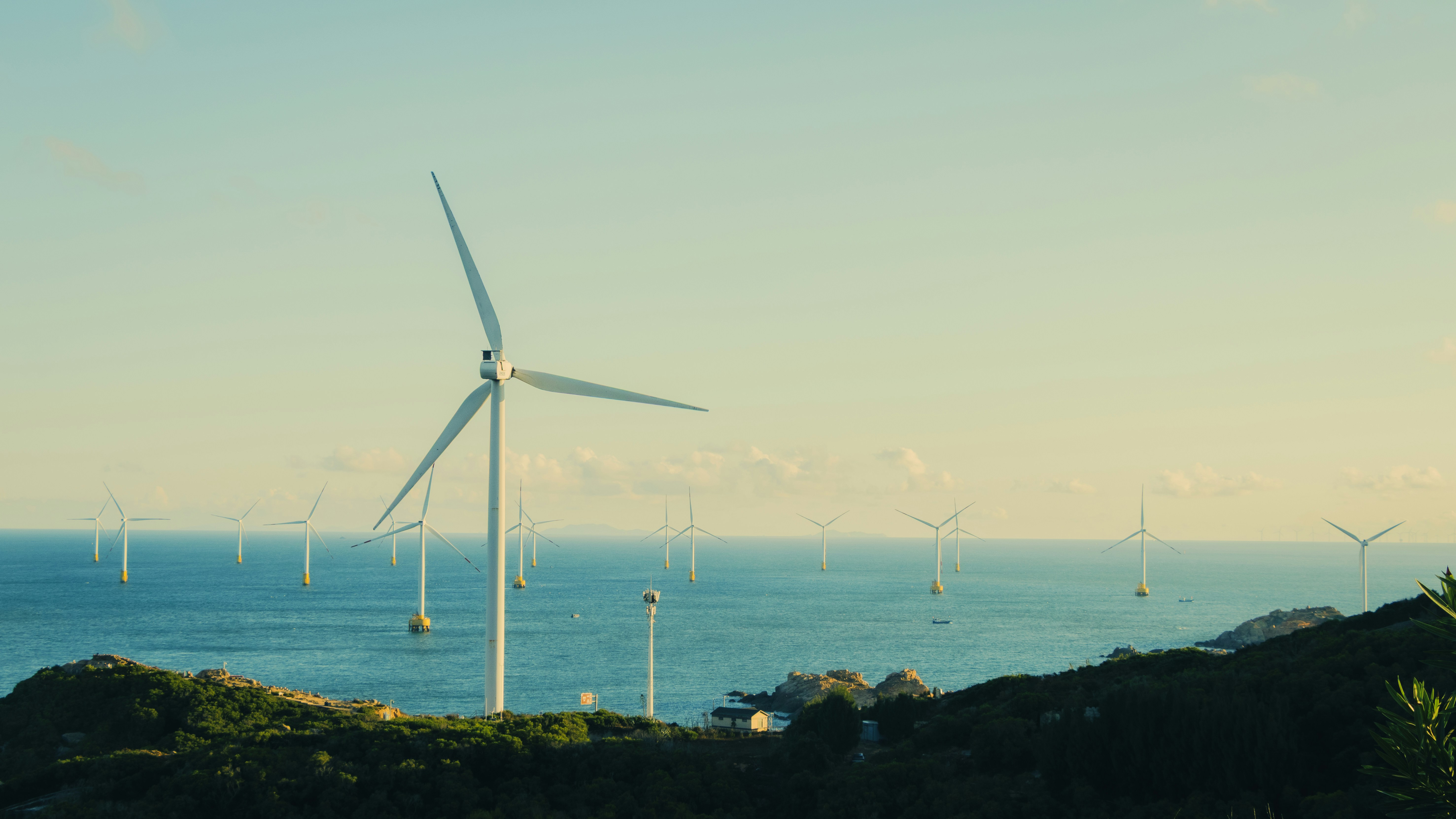 Wind turbines stand tall against a serene ocean backdrop, illustrating the fusion of technology and nature's energy potential.