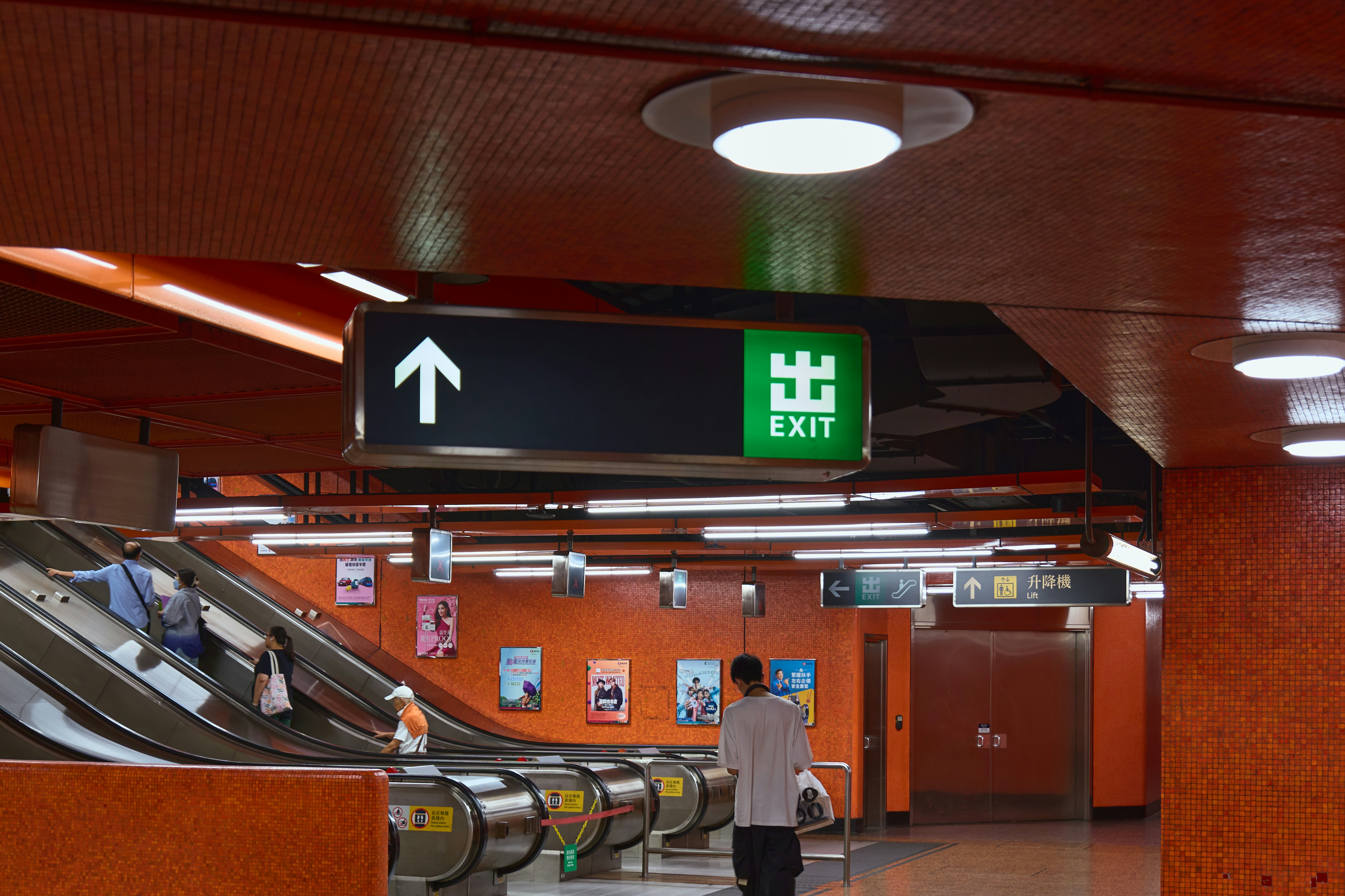 An illuminated exit sign above escalators in a subway station. photo ...